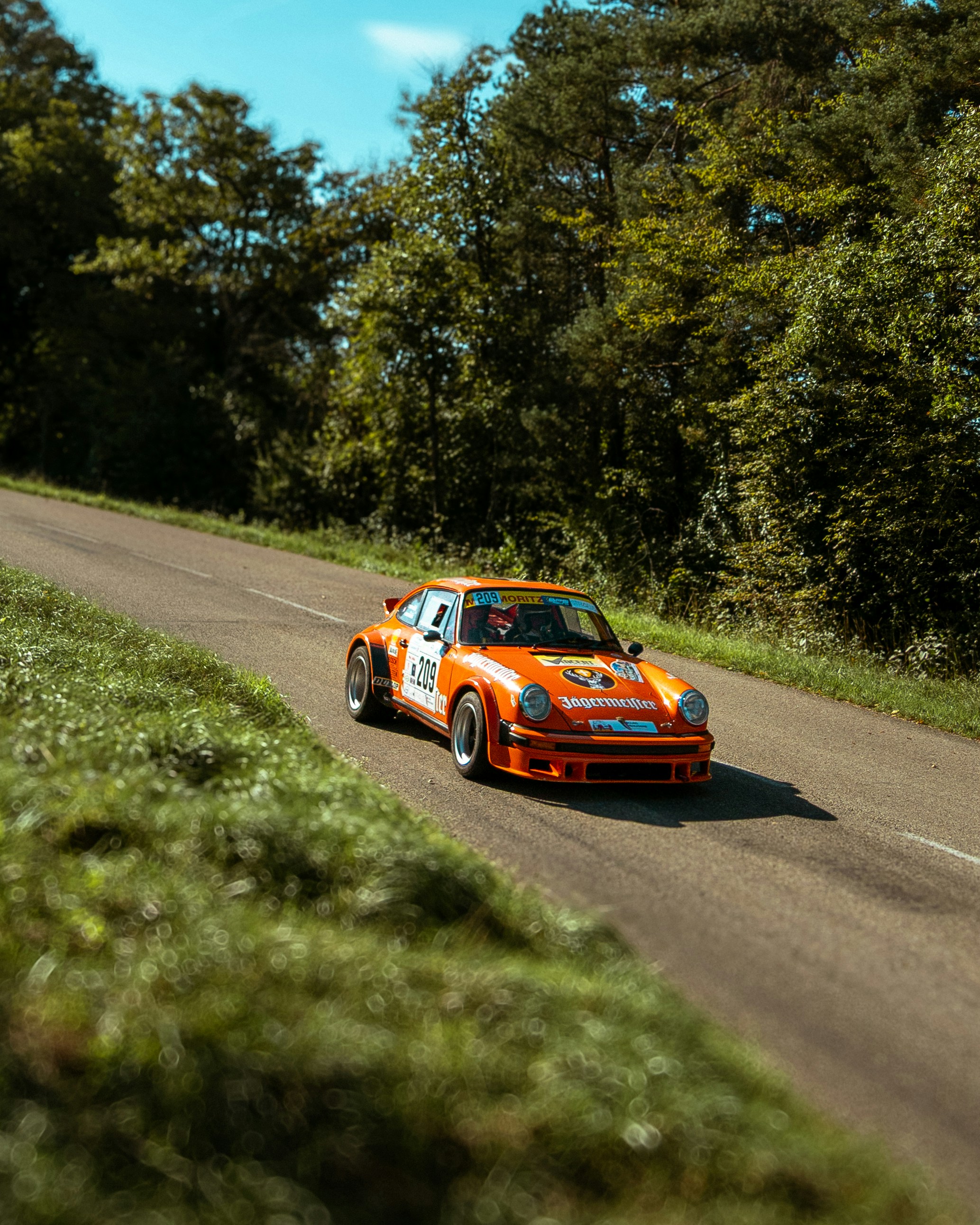 Orange vintage race car driving on a winding road.