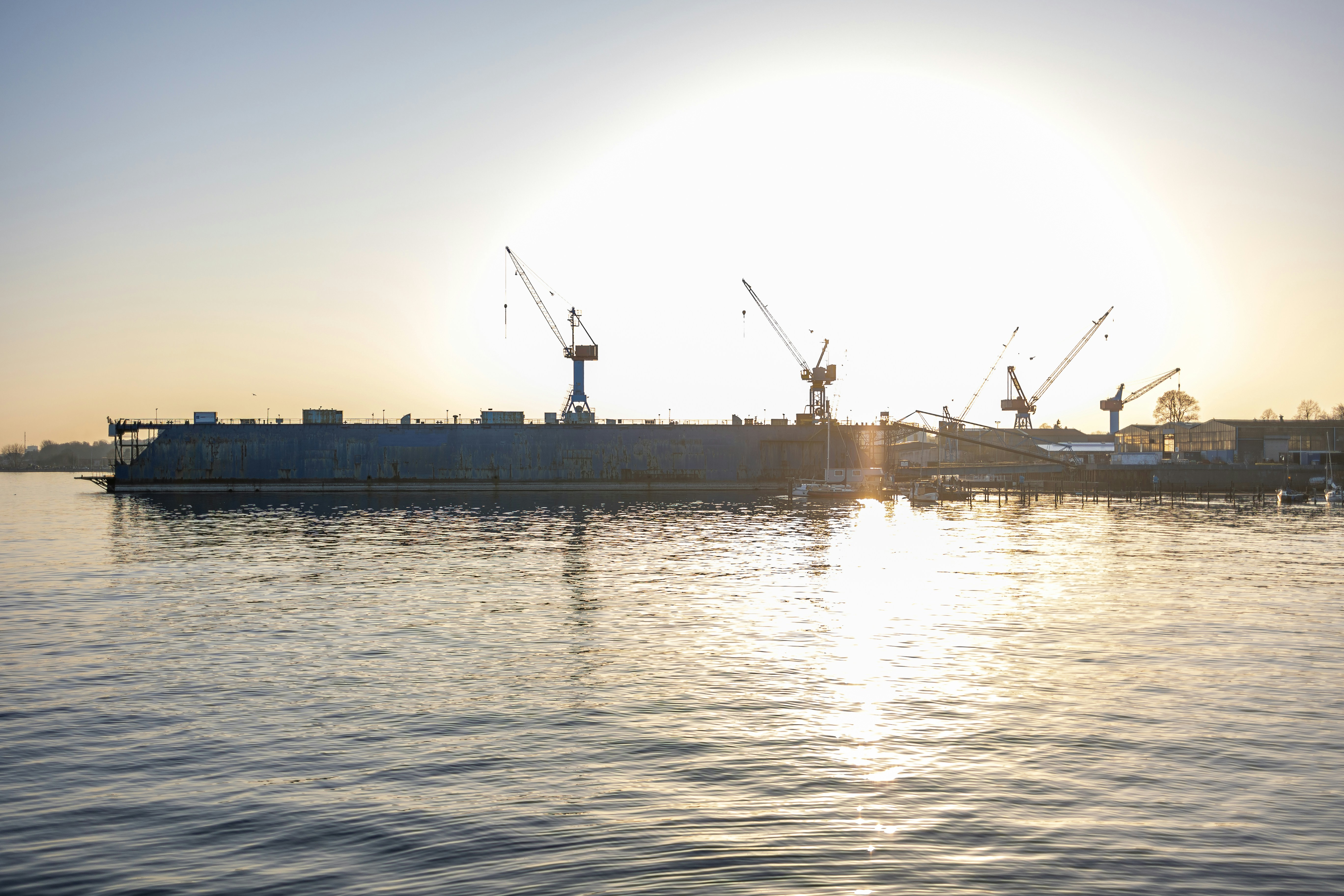 Shipyard with cranes at sunset over water.