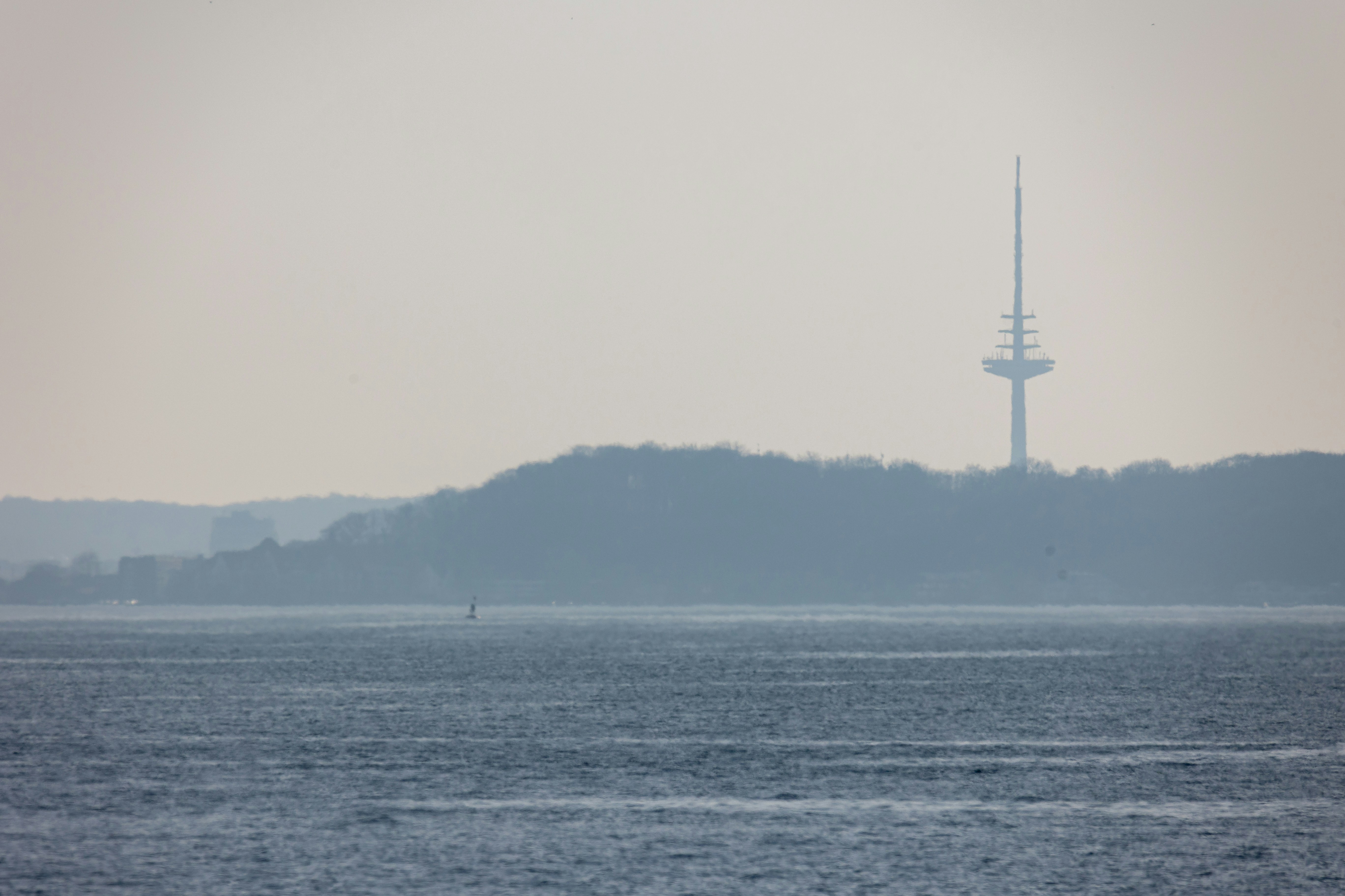A distant radio tower on a hazy coastline.
