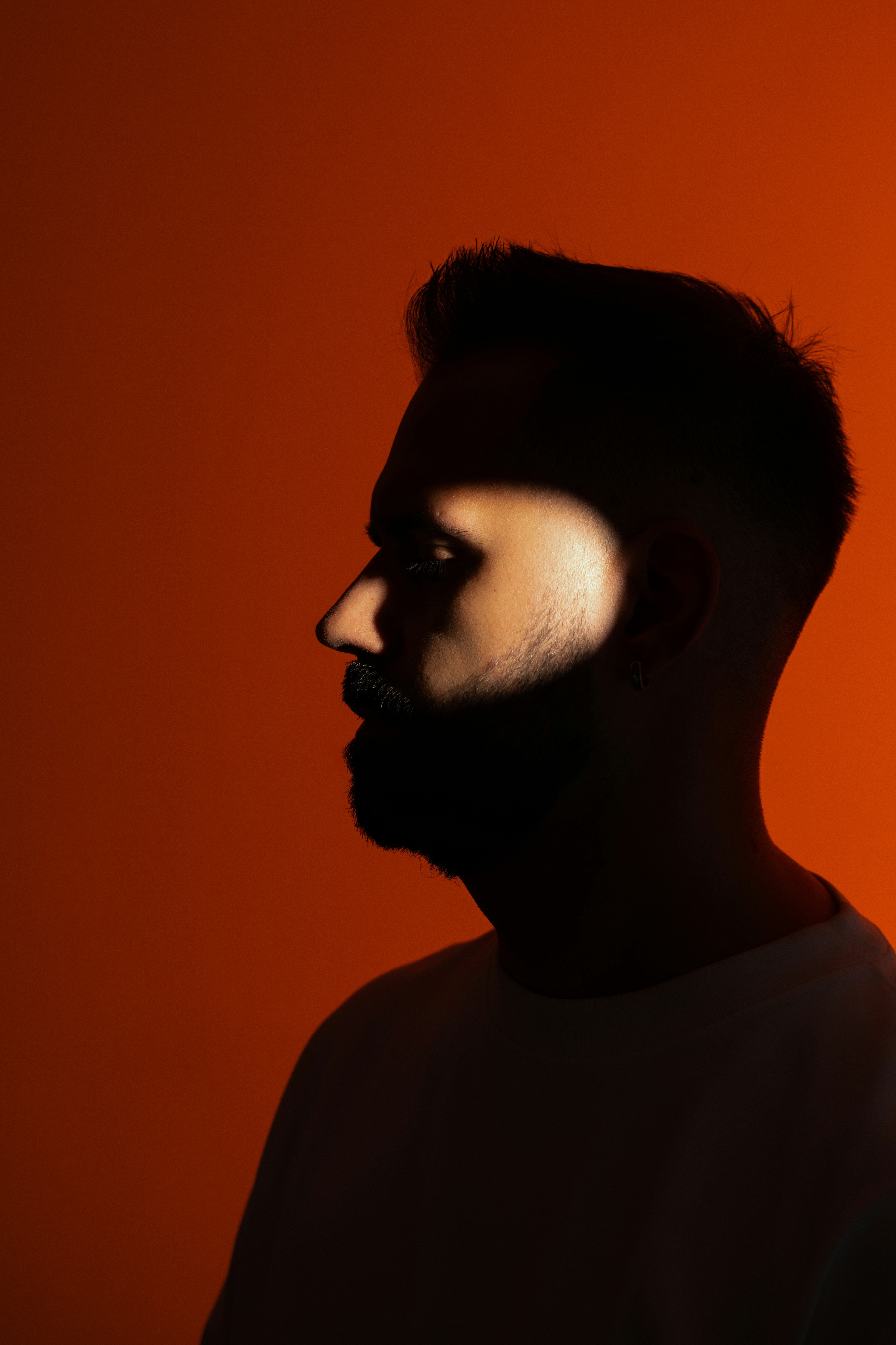 Profile of a man in silhouette, illuminated by a dramatic light source against a vibrant orange background.