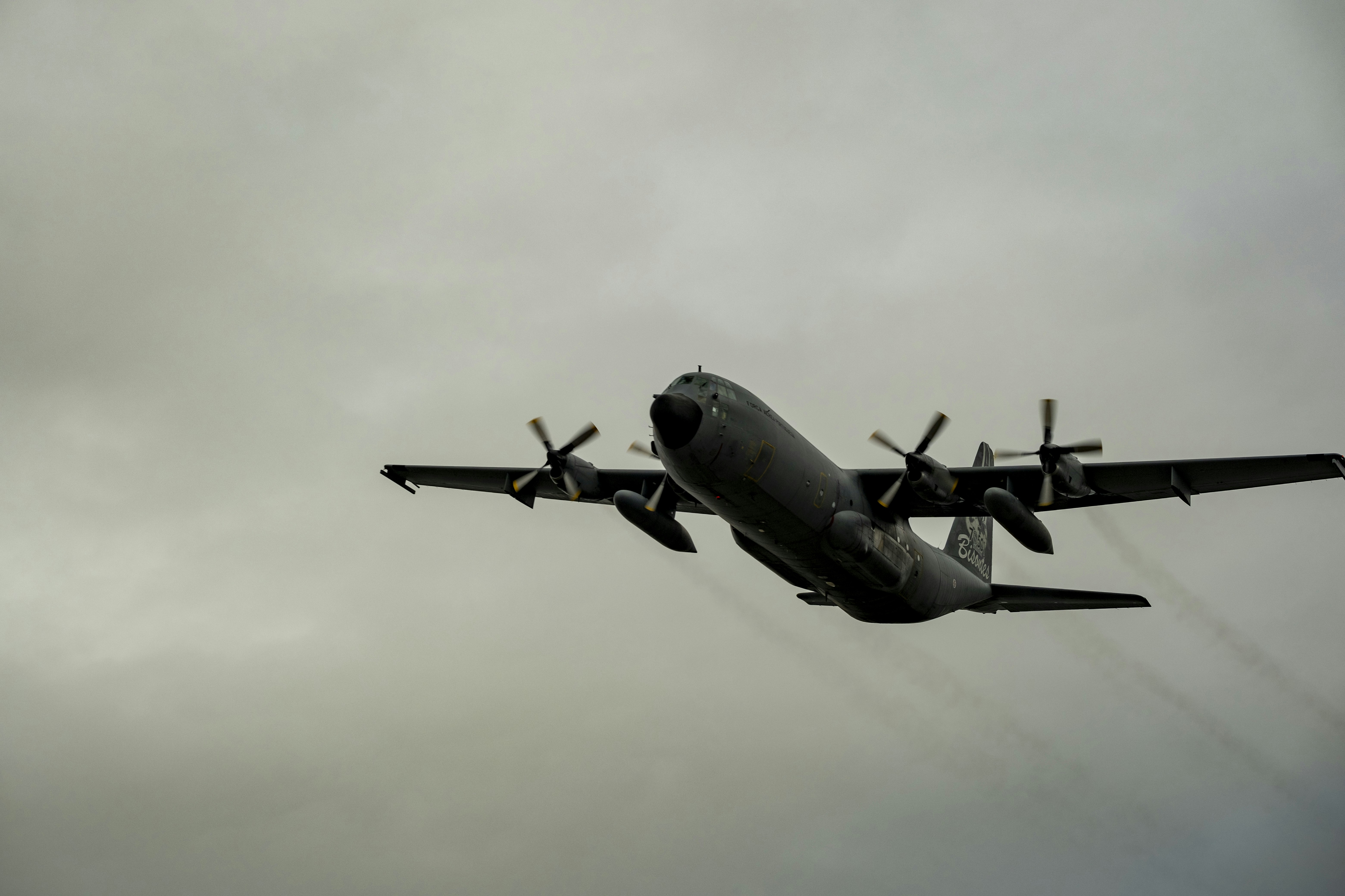 A military cargo plane flies through cloudy skies.
