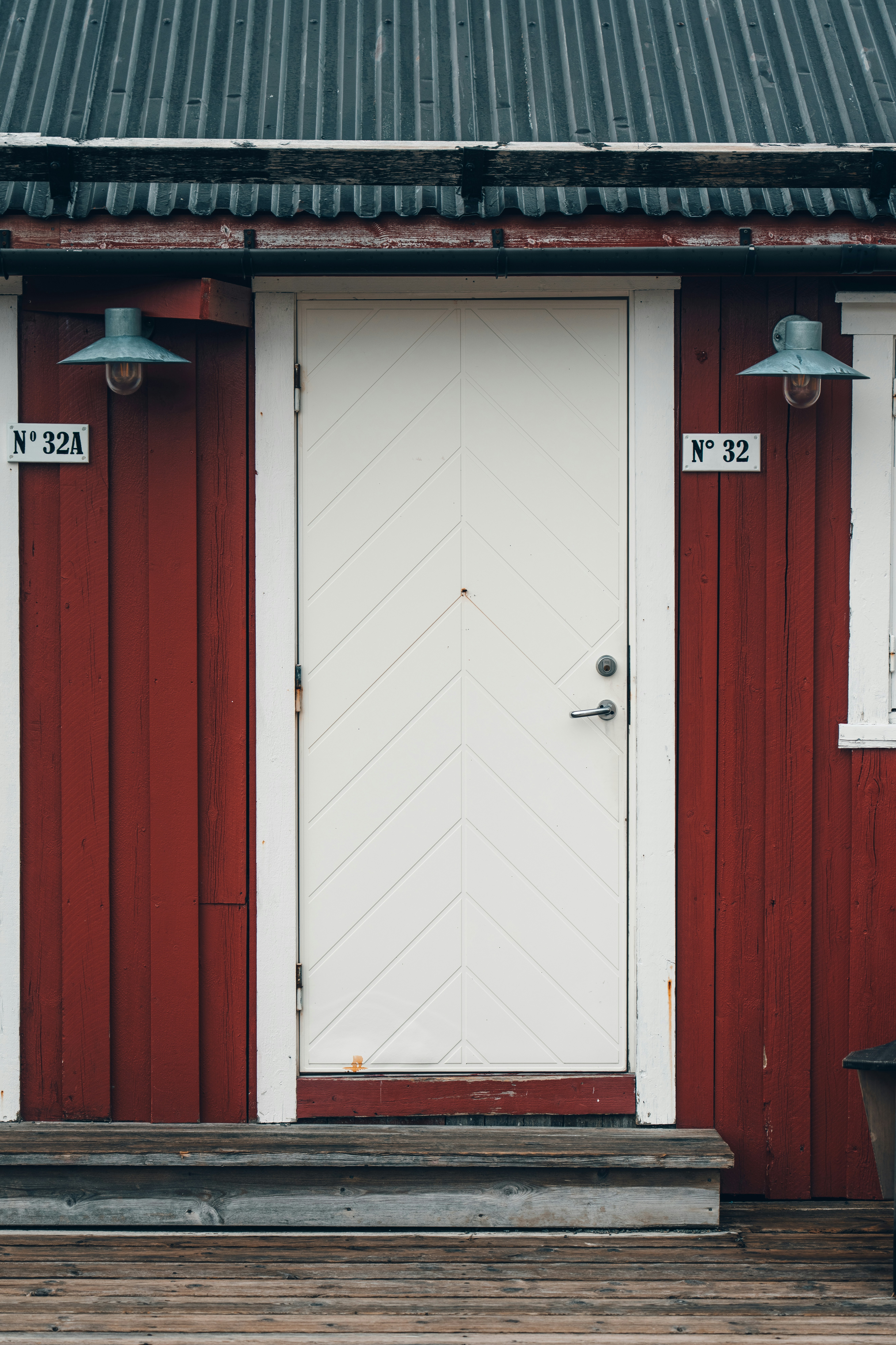 Die weisse Tür in den Nächsten Raum | Red wooden cabin with a white door and lamps.