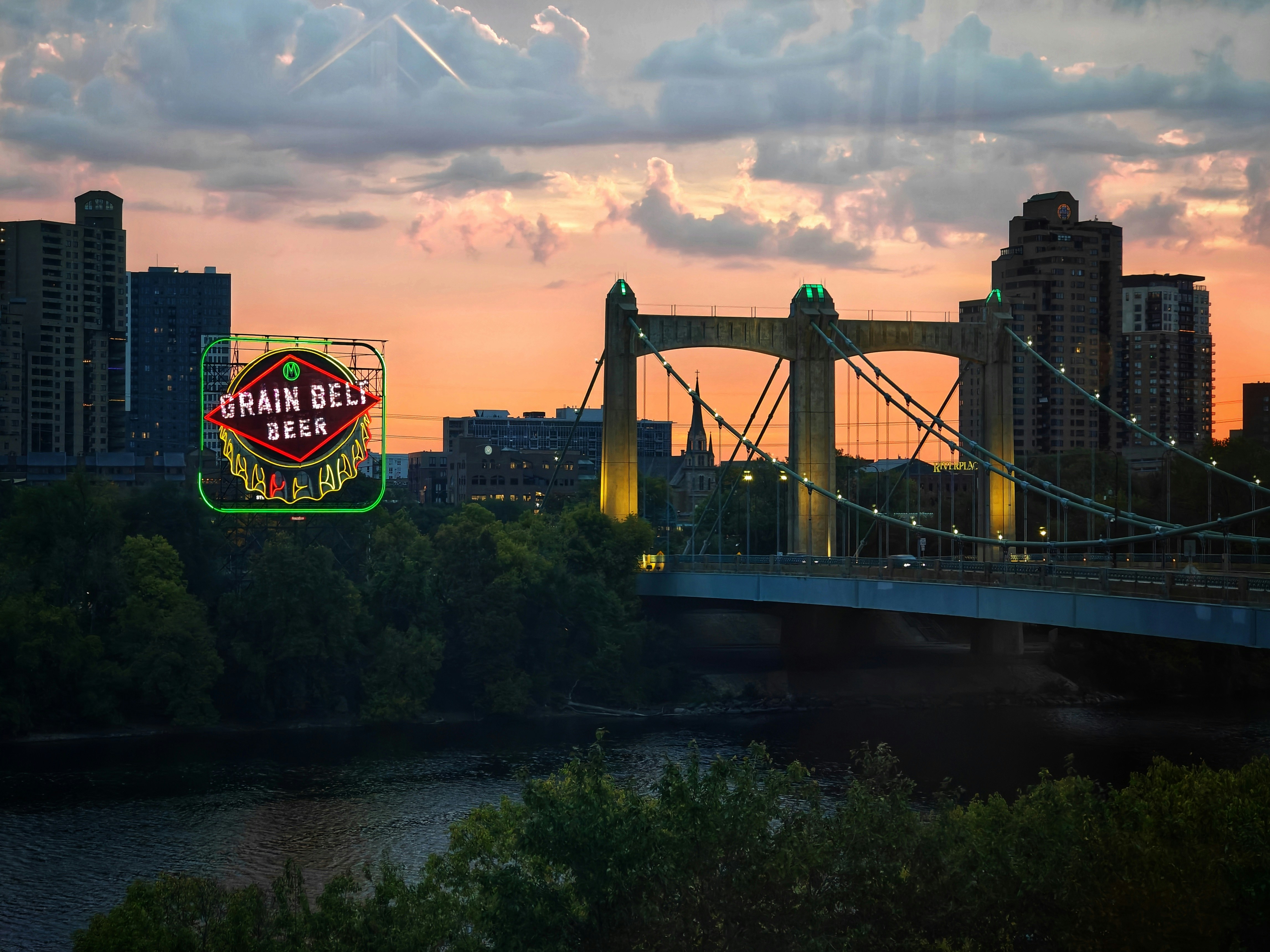 Overlooking the Hennepin Bridge in Minneapolis ft. the Mississippi River & Grain Belt Beer neon sign. | City skyline with bridge and neon beer sign at sunset.