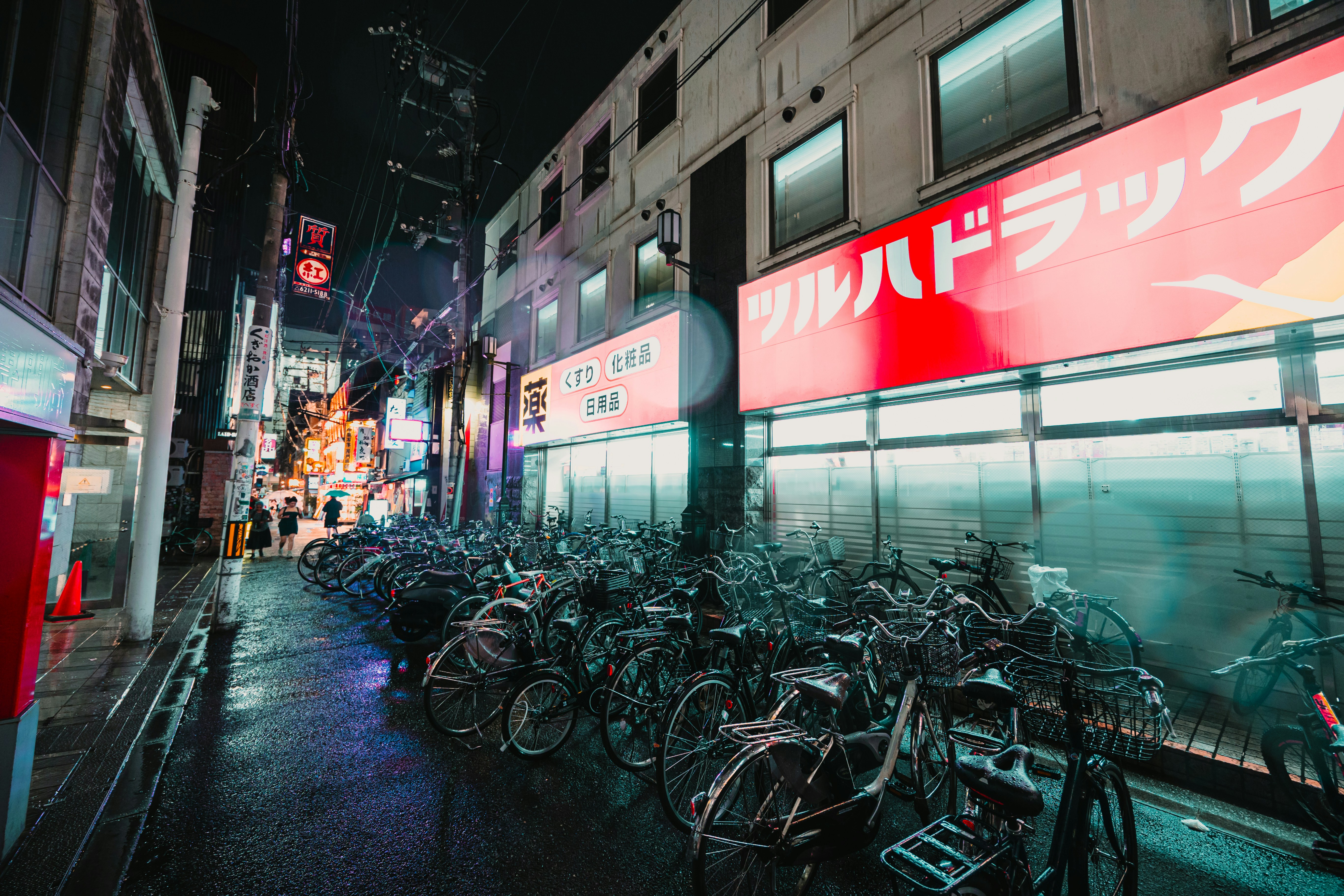 A bustling alley filled with parked bicycles under vibrant neon signs, showcasing the urban nightlife. The reflections on the wet pavement add to the atmosphere.