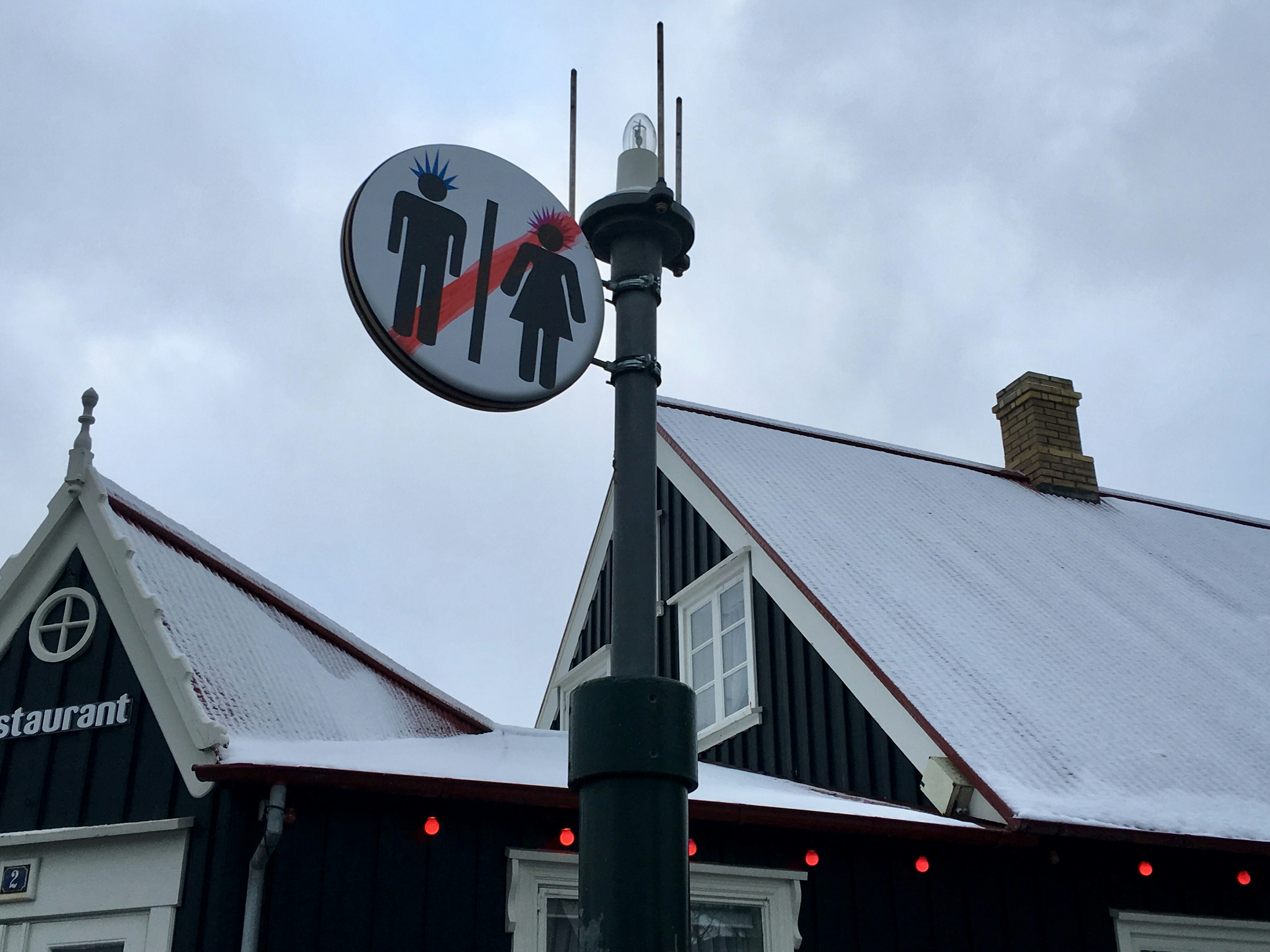 Circular Restroom Sign on a Snow-Dusted Lamppost by a Chalet-Style Inn