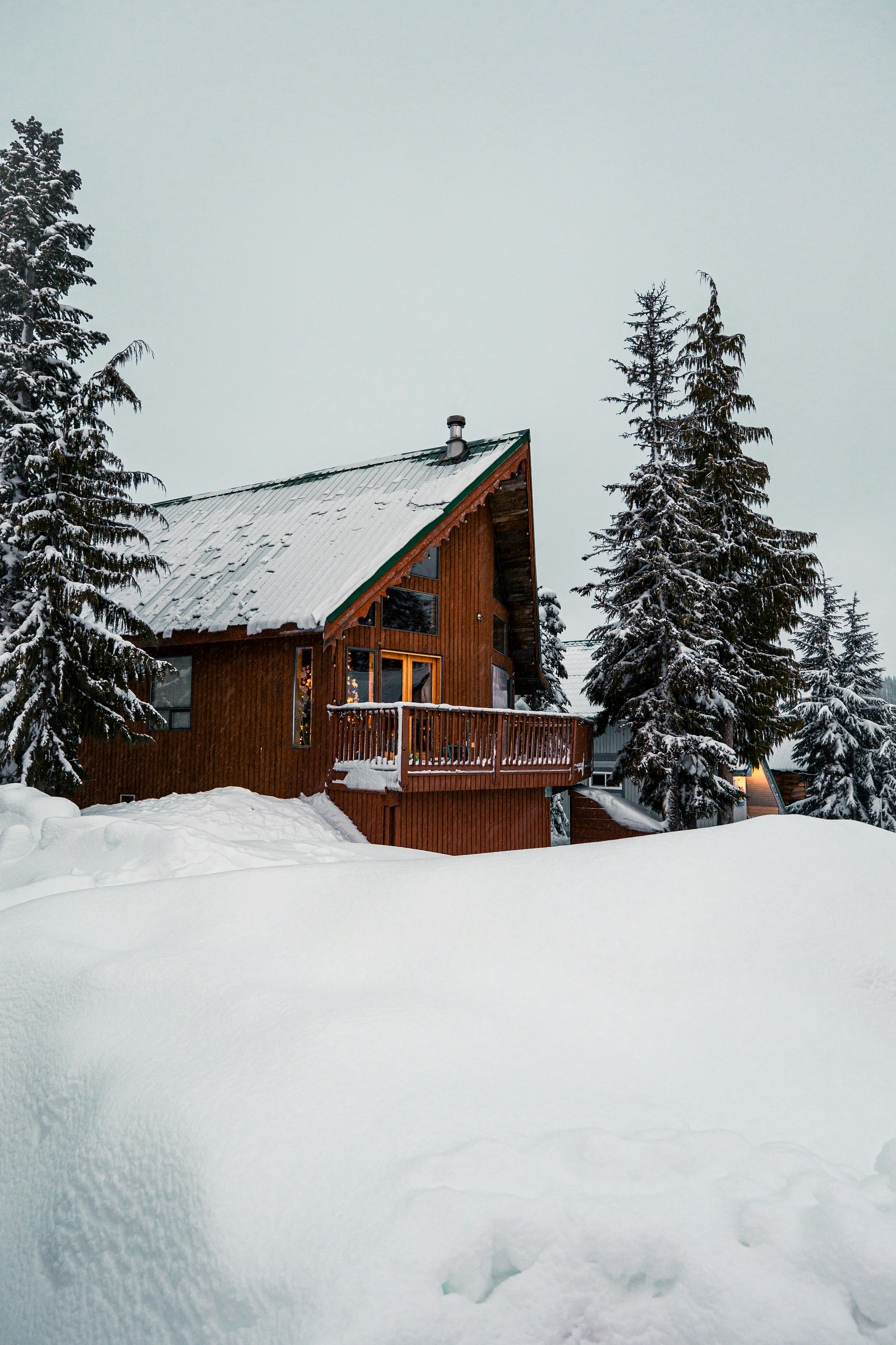 A charming wooden cabin nestled in a snowy landscape, surrounded by tall evergreen trees under a soft, overcast sky.
