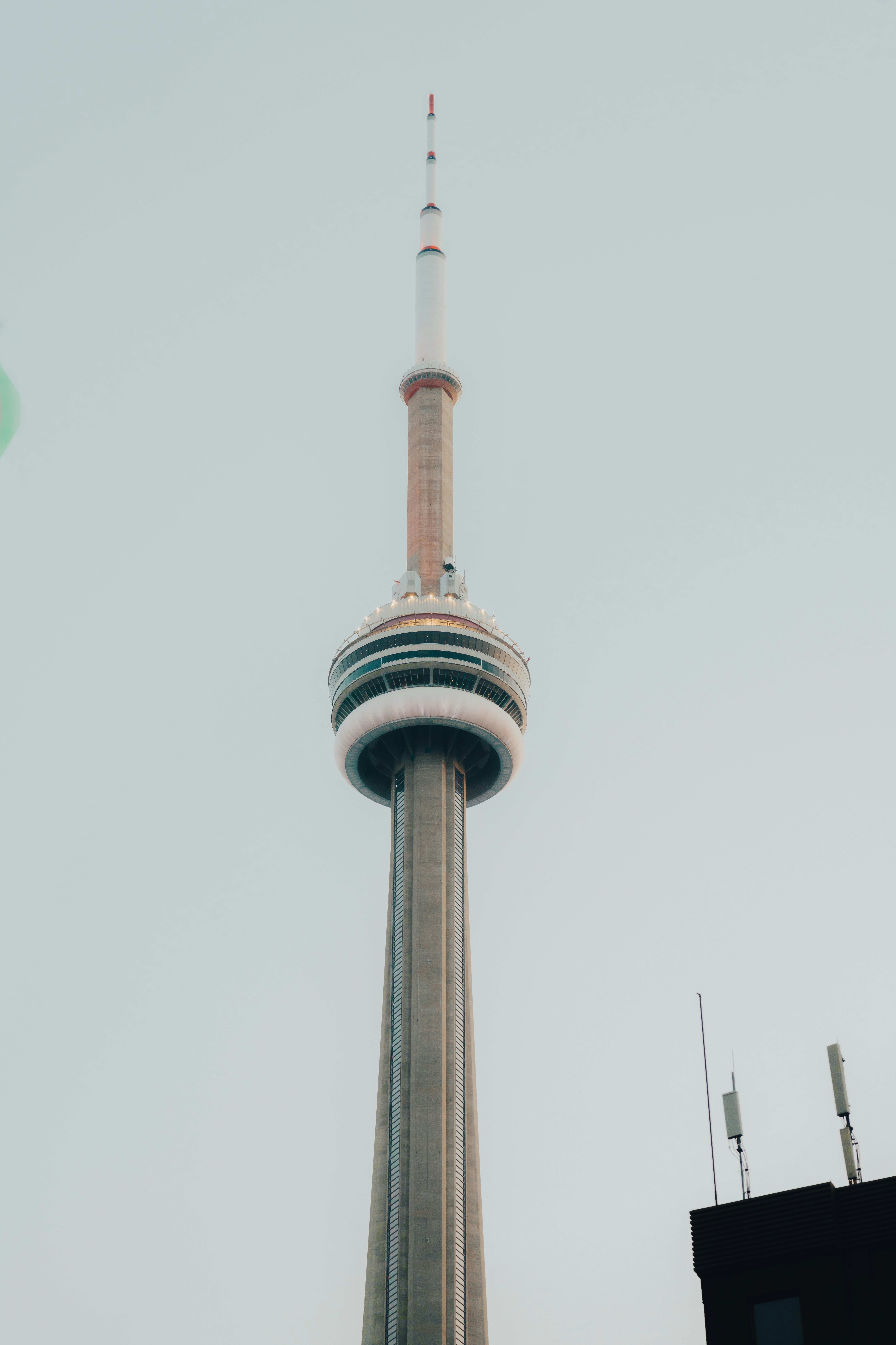 The CN Tower rises majestically against a pale sky, showcasing its distinctive architecture and observation deck. A nearby building adds urban context.