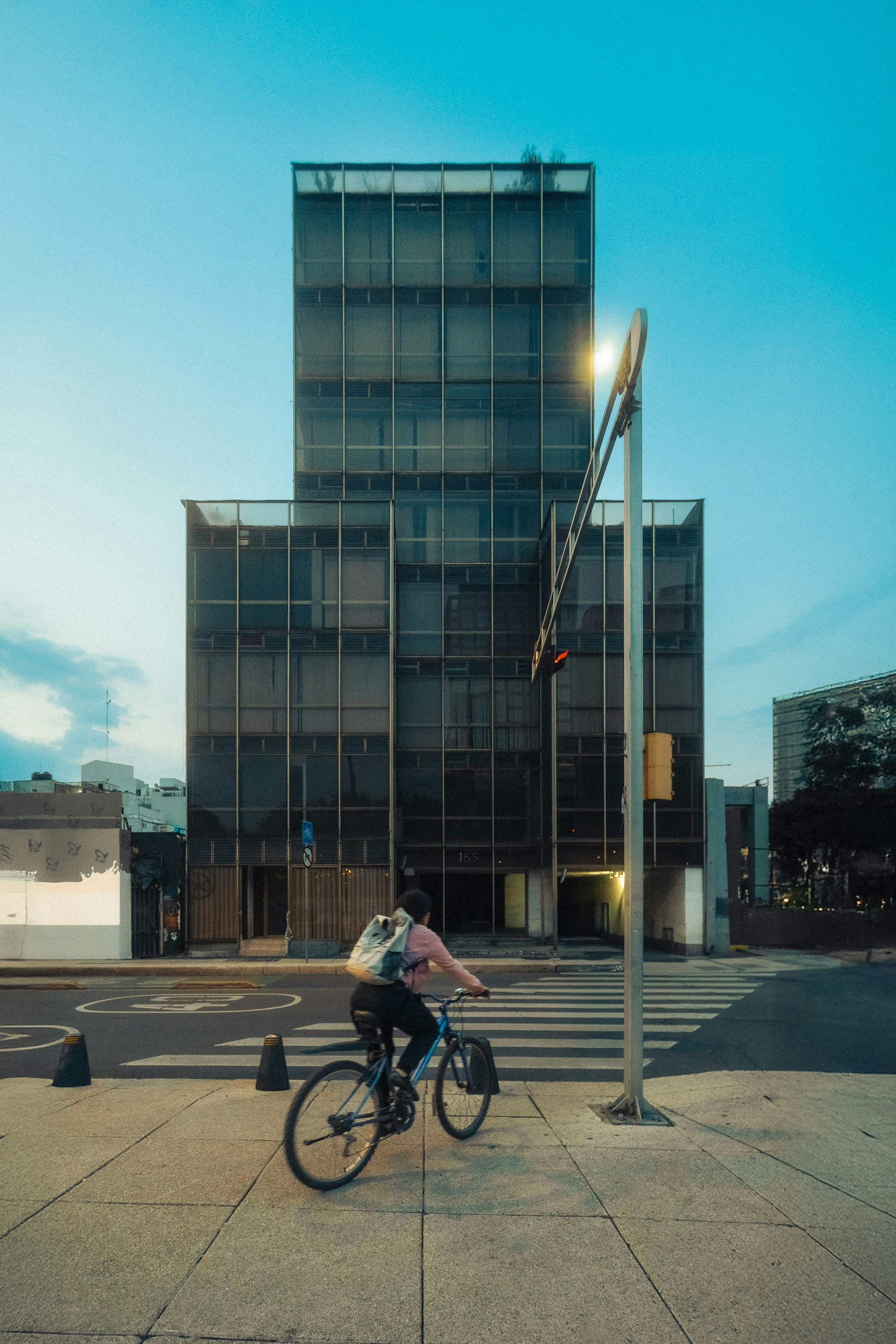 Person rides bicycle past modern building at dusk