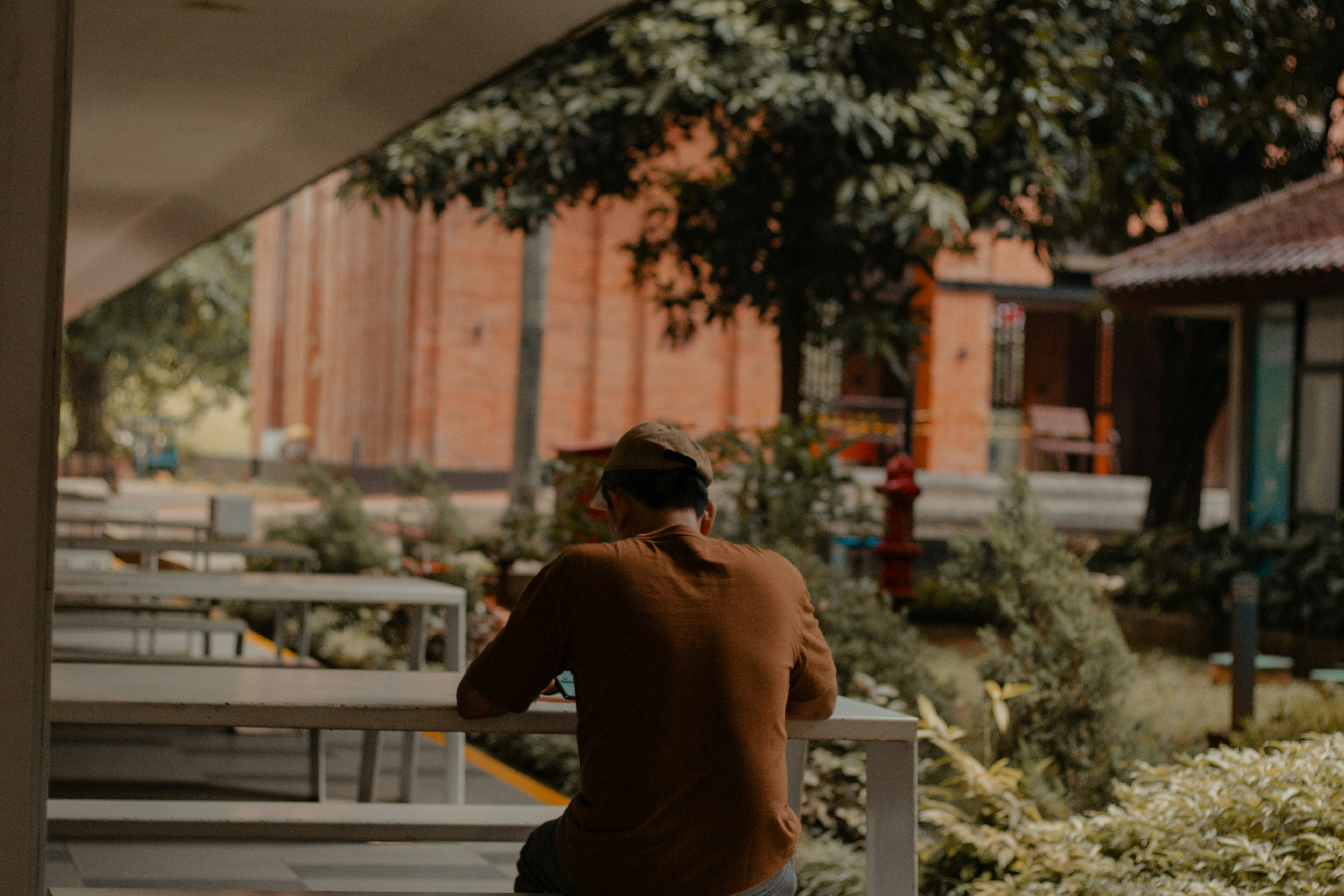 Person sitting next to garden in Universitas Indonesia | Man sitting at an outdoor table, looking away.
