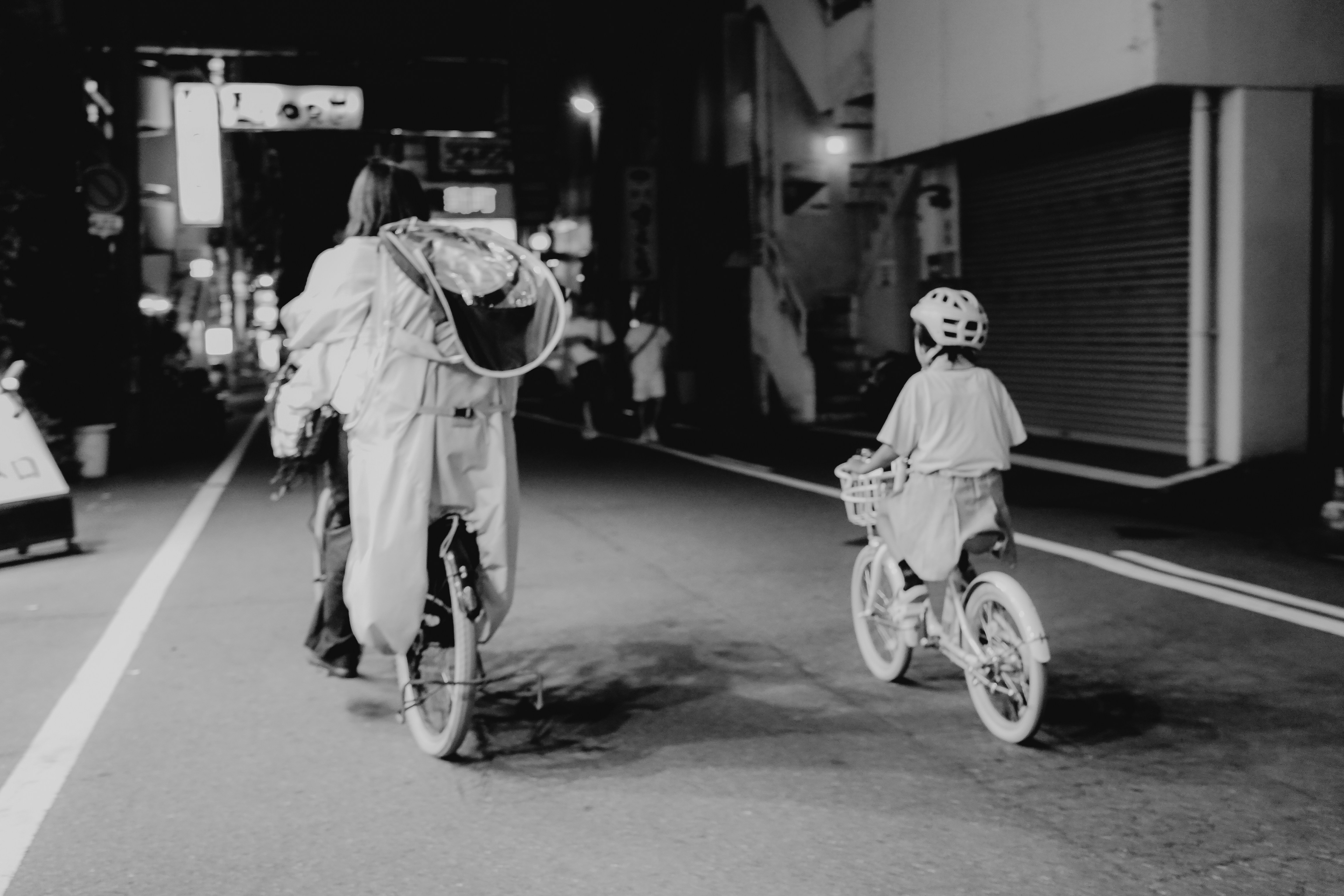Two people riding bicycles down a dark street.