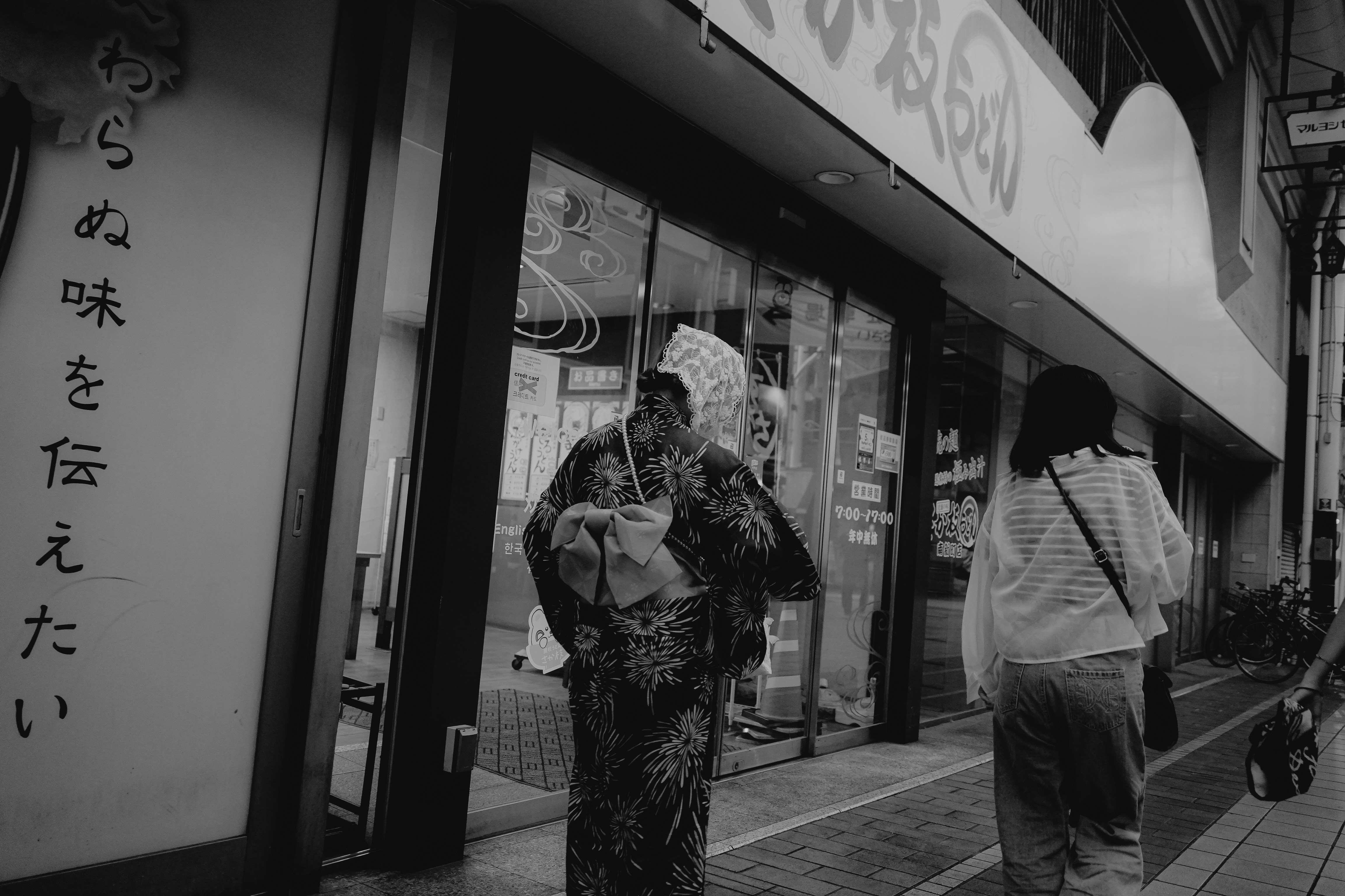 Two figures stroll through a lively street, one adorned in traditional attire, while the other embraces modern fashion. The scene captures the blend of past and present.
