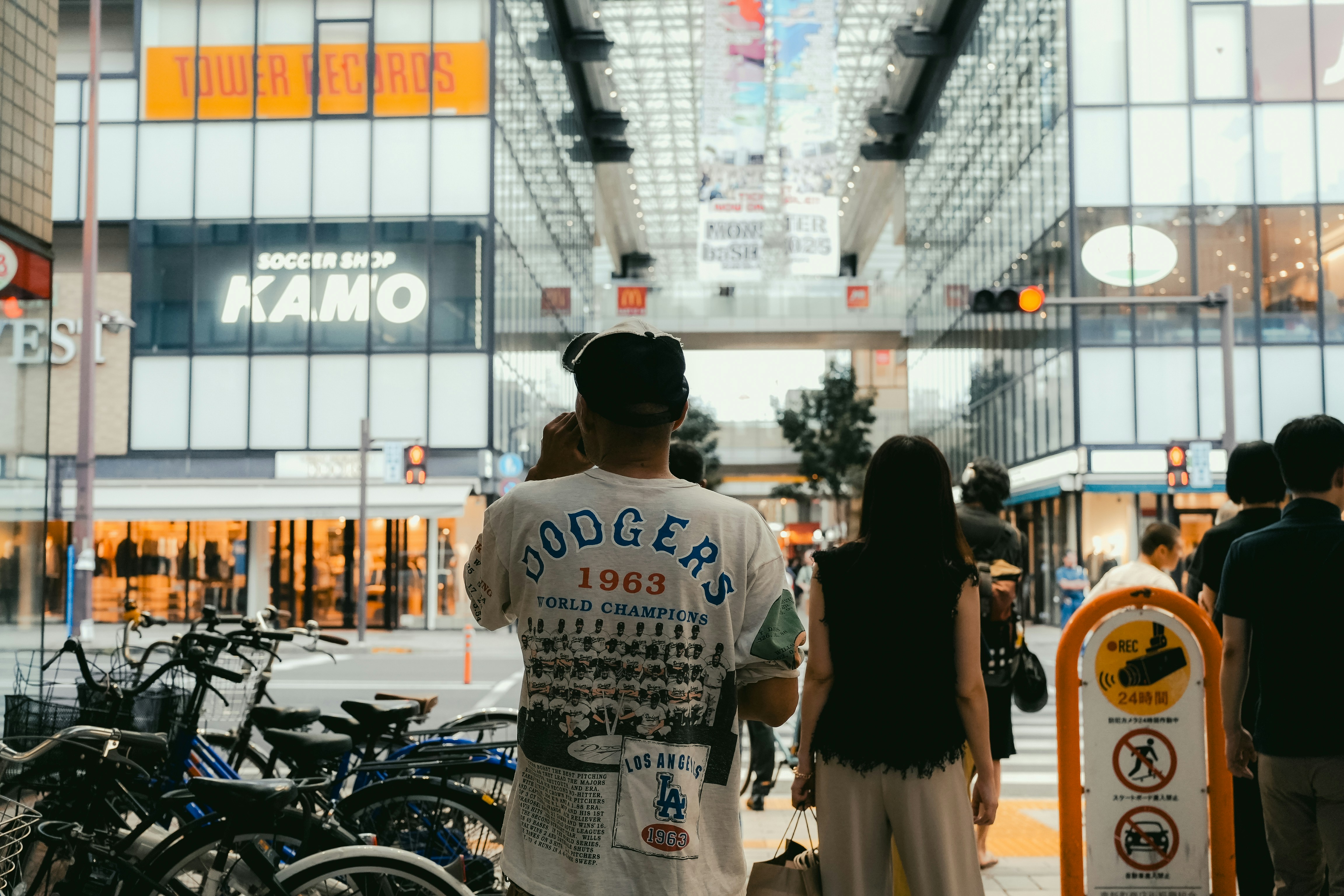 Dodgers Jacket at the Glass-Walled Crosswalk: A Quiet Moment in a Neon City