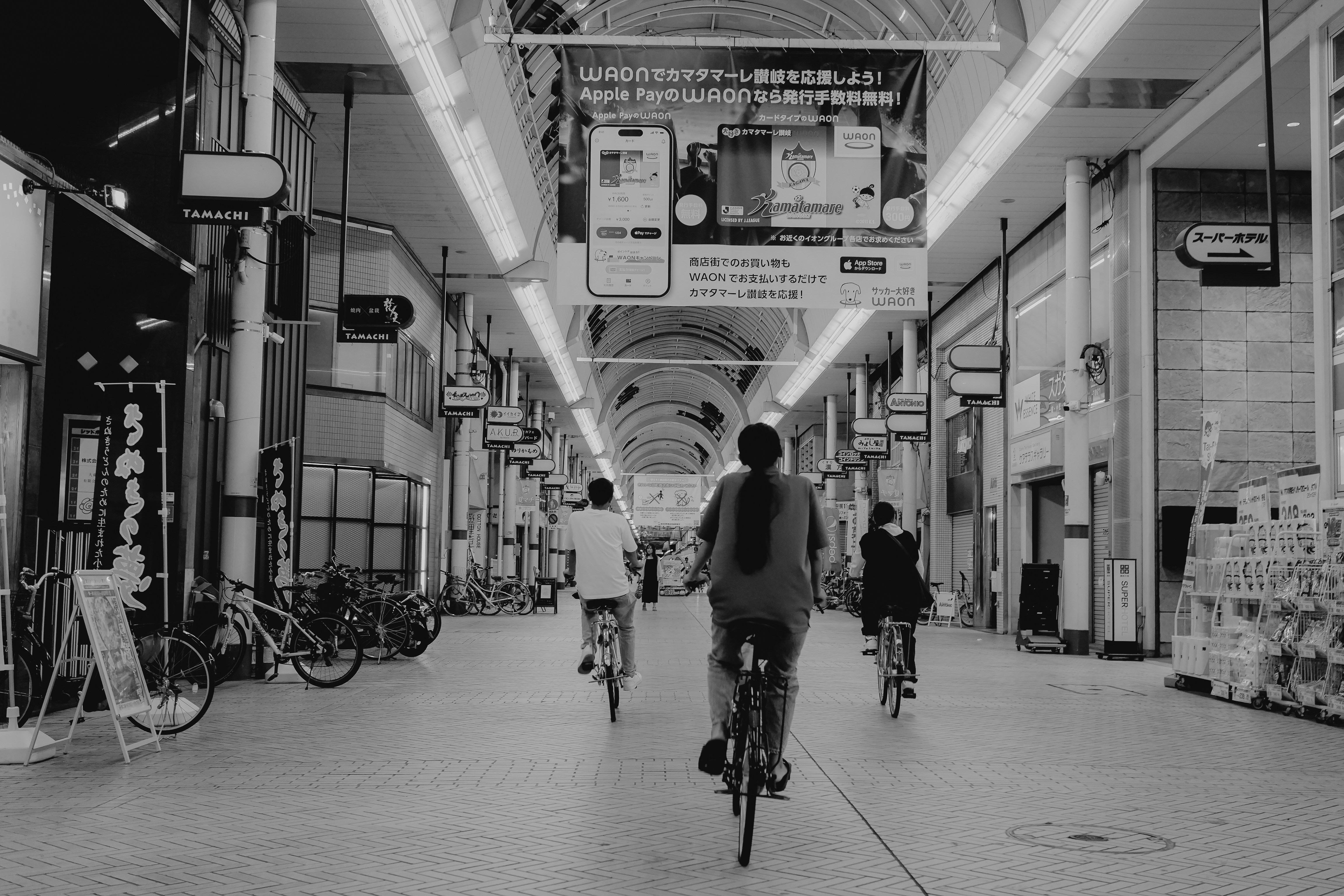 Monochrome Arcades: Cyclists Glide Through a Luminous Indoor Market