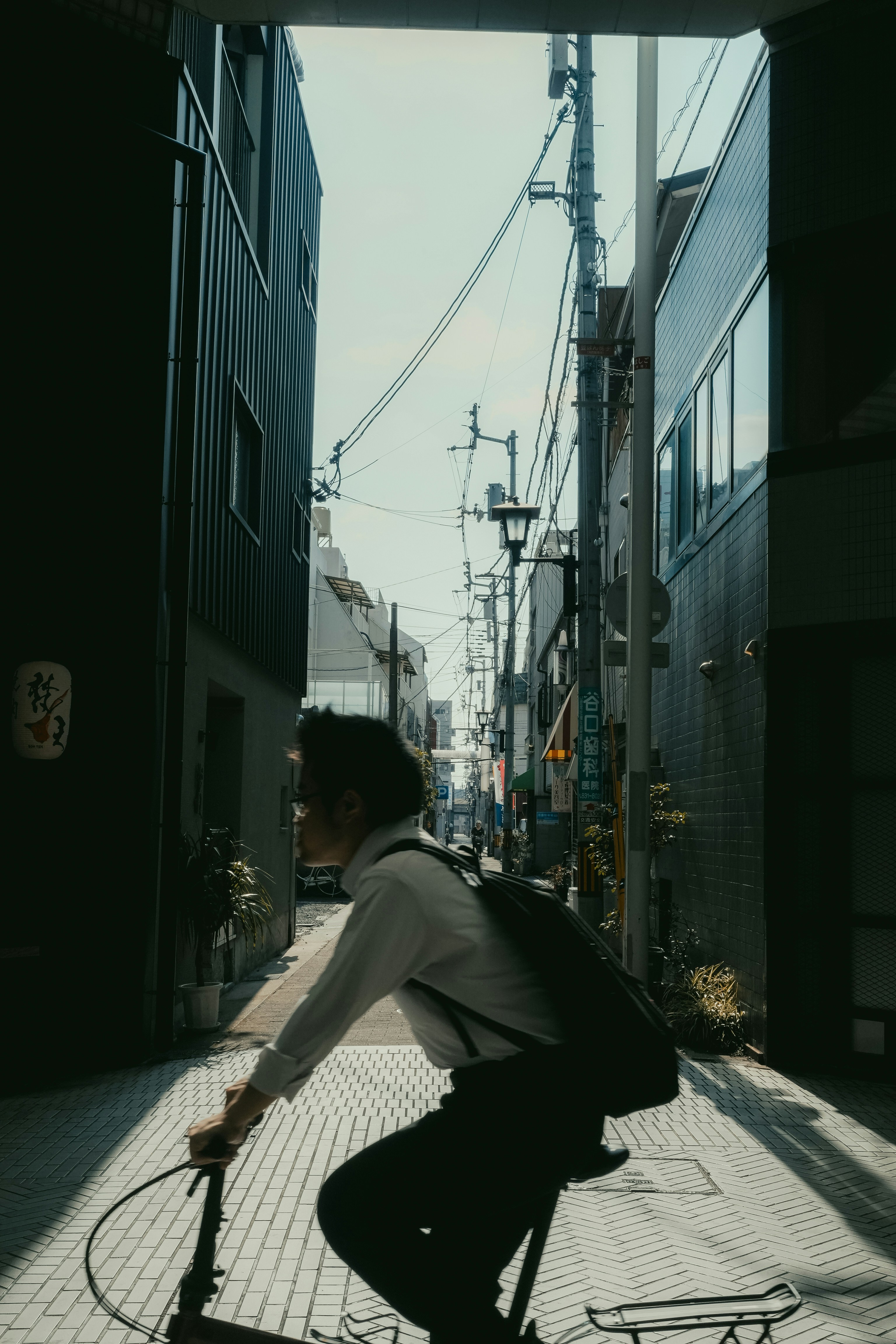 Man riding bicycle down narrow sunlit alley.