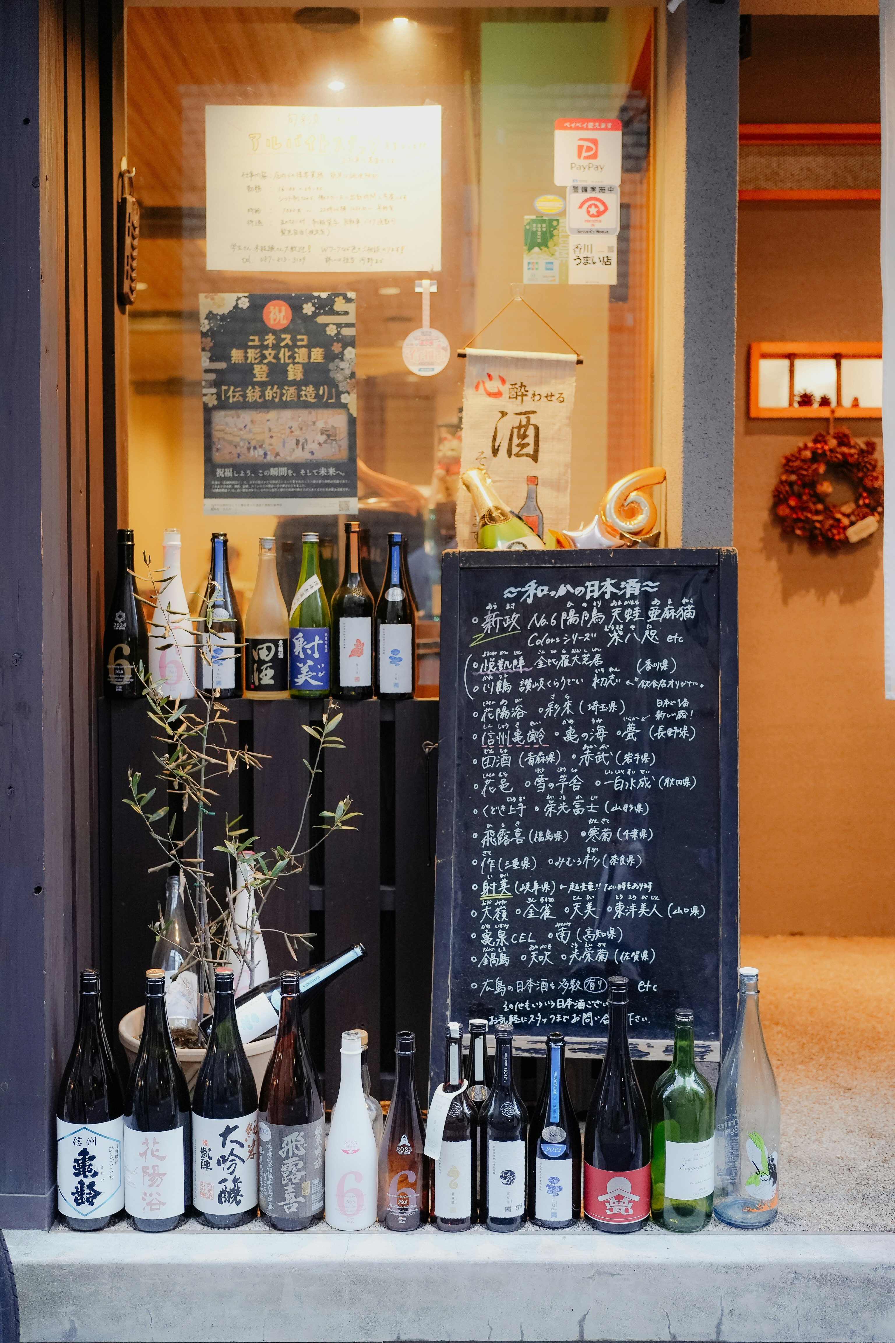 A charming display of assorted sake bottles alongside a handwritten menu, showcasing traditional Japanese beverages. The inviting storefront hints at a cozy dining experience.