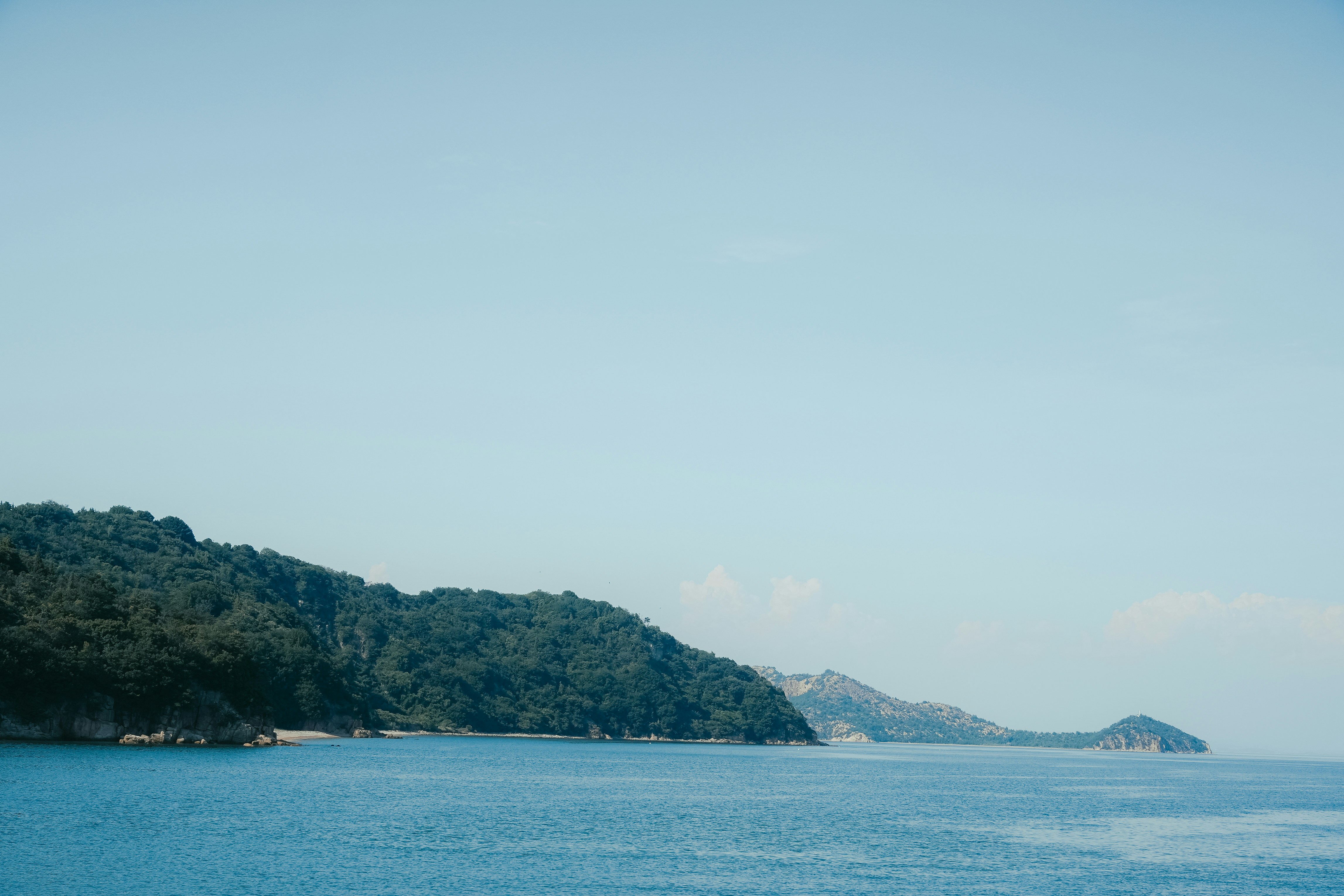 Green island coastline meets calm blue ocean water.