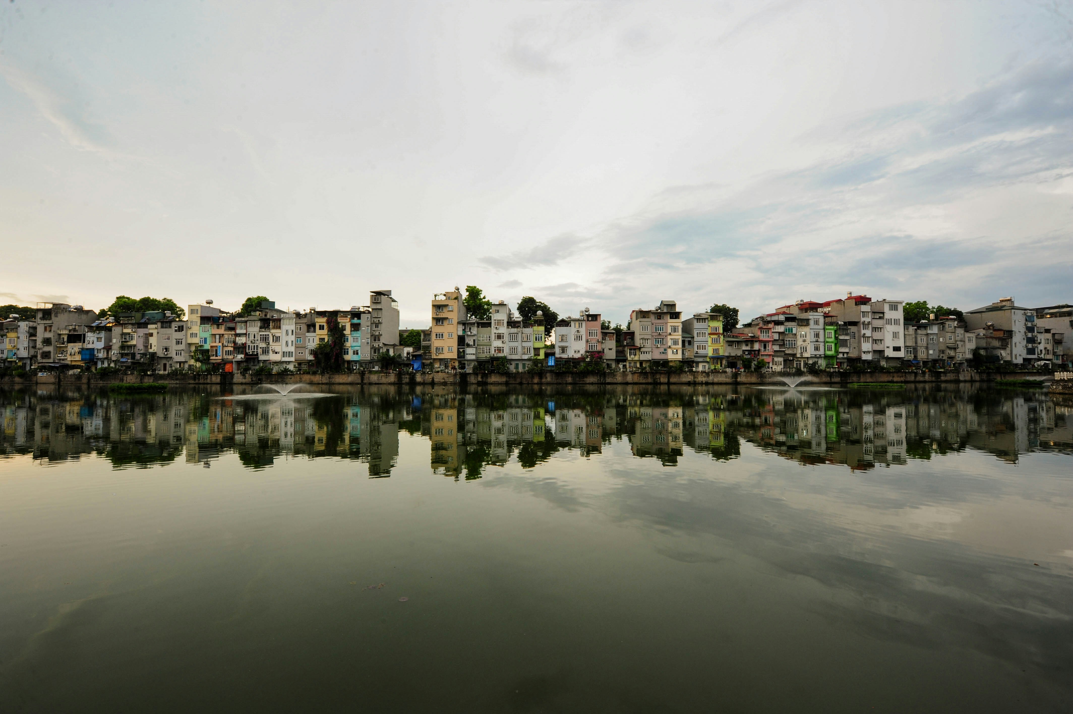 Buildings reflected in calm water under cloudy sky