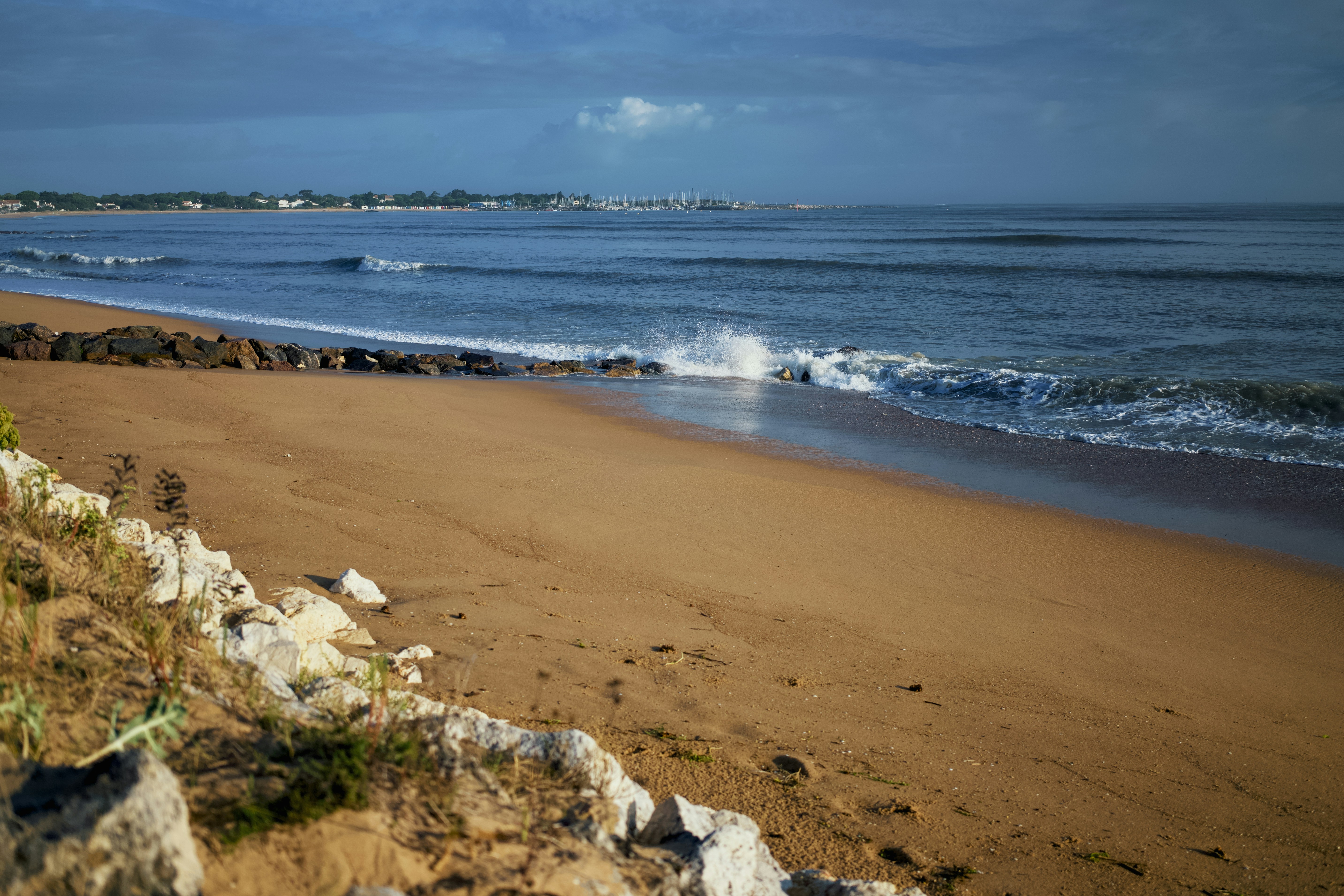 Sandy beach with gentle waves and distant town.