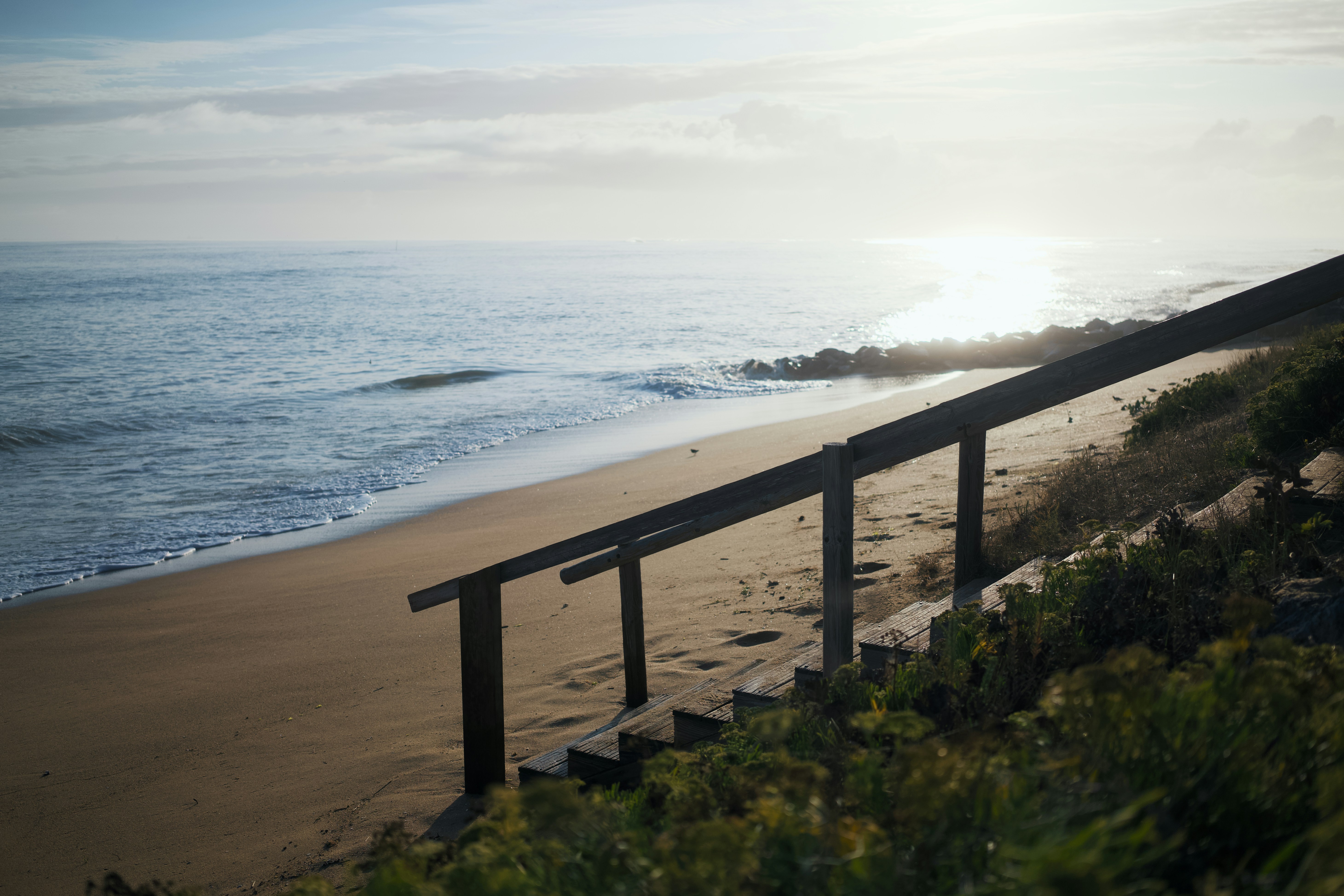 Wooden steps leading down to a tranquil beach with gentle waves lapping at the shore under a soft morning light.