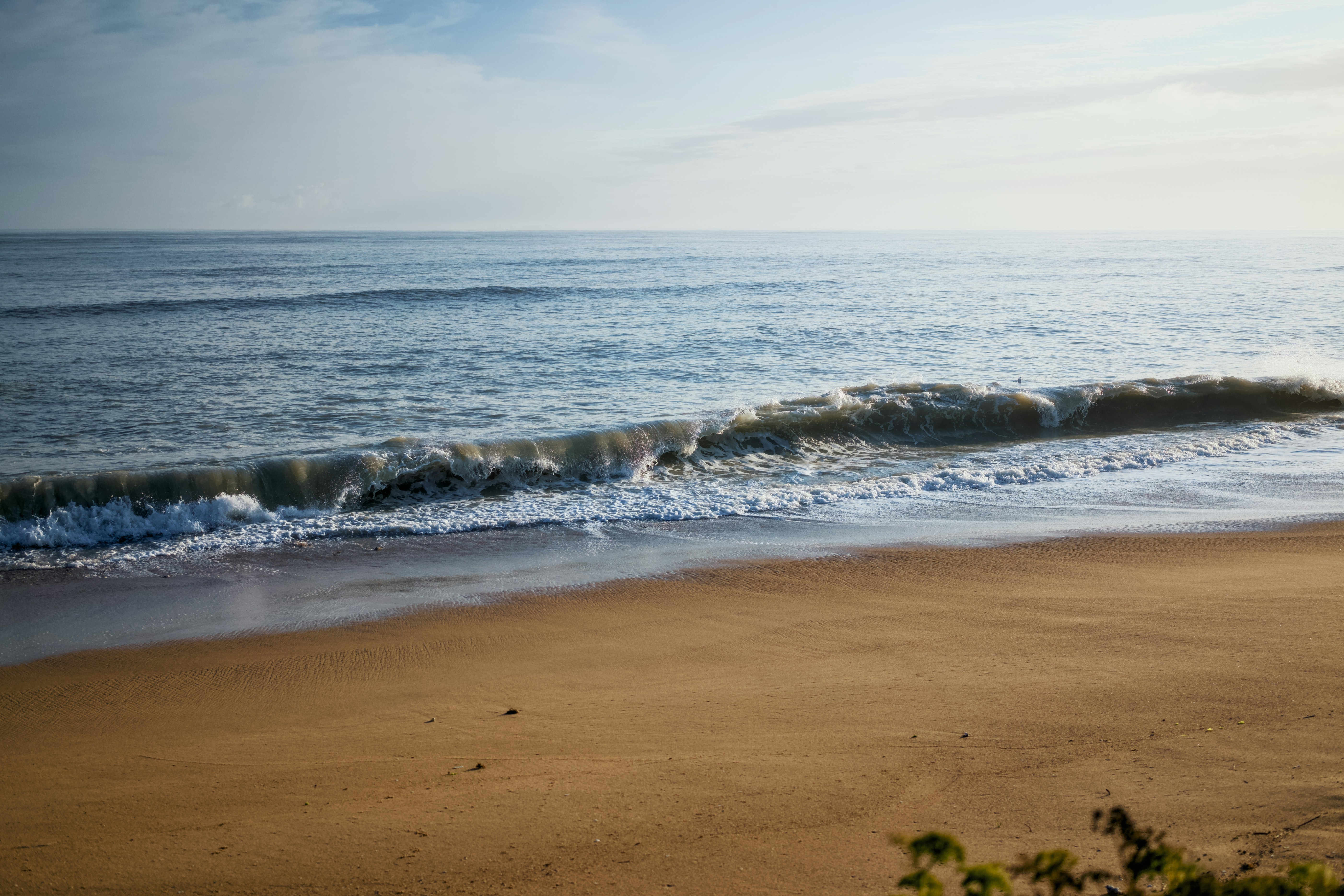 Gentle waves roll onto a sandy beach at dawn.