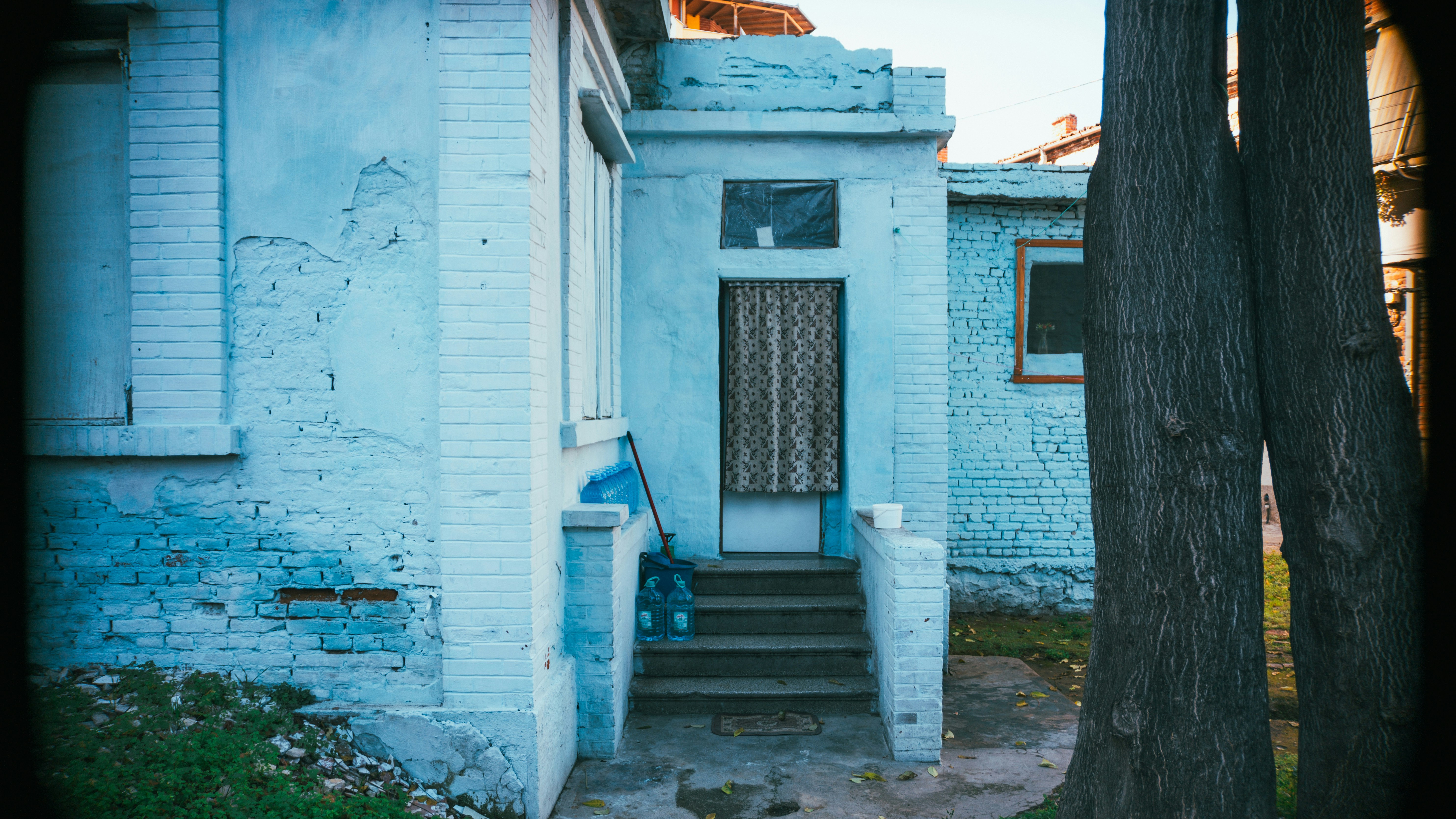 Light blue weathered building with a doorway and steps.