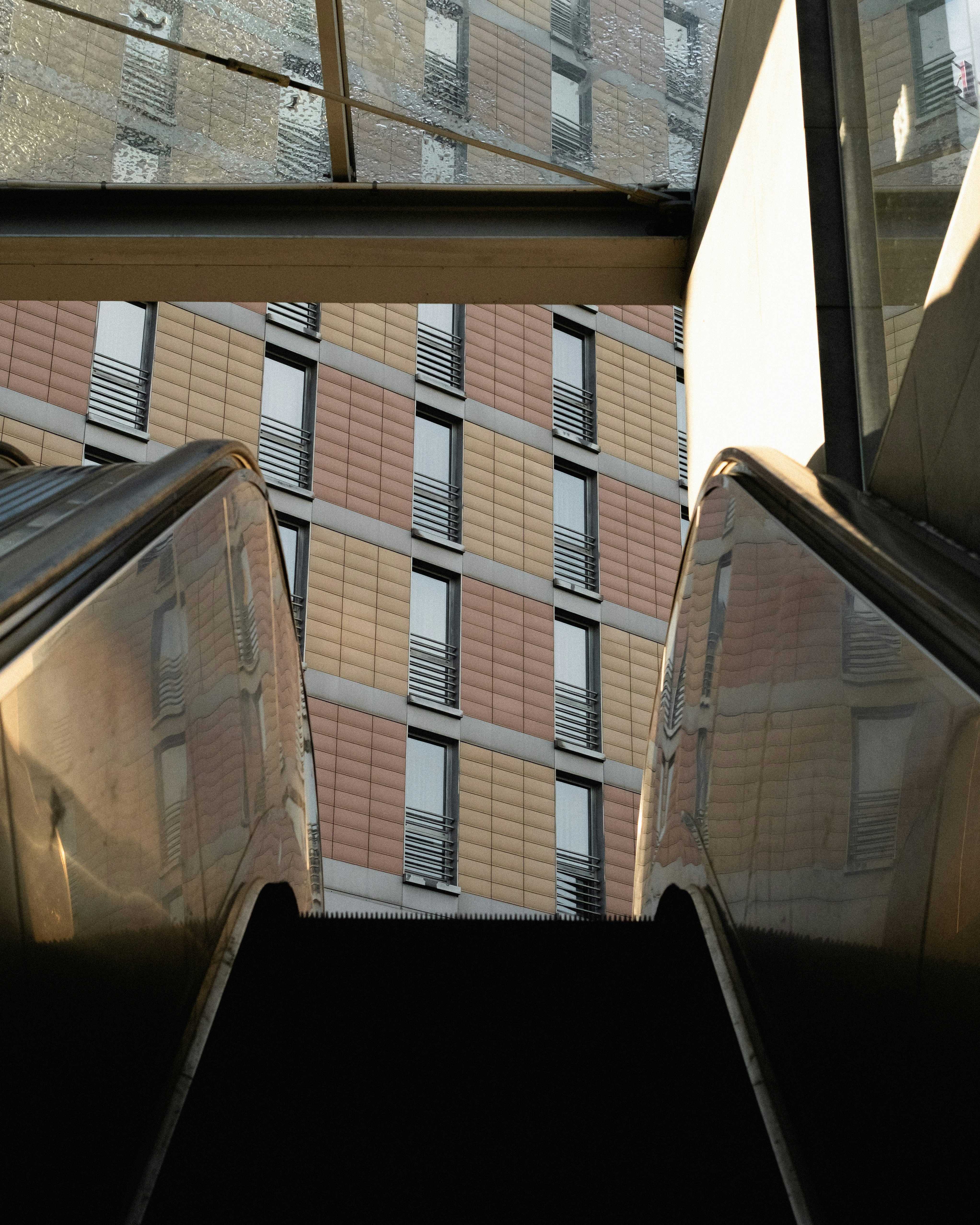 Escalator leading upward with reflections of a contemporary building facade featuring colorful panels and windows.