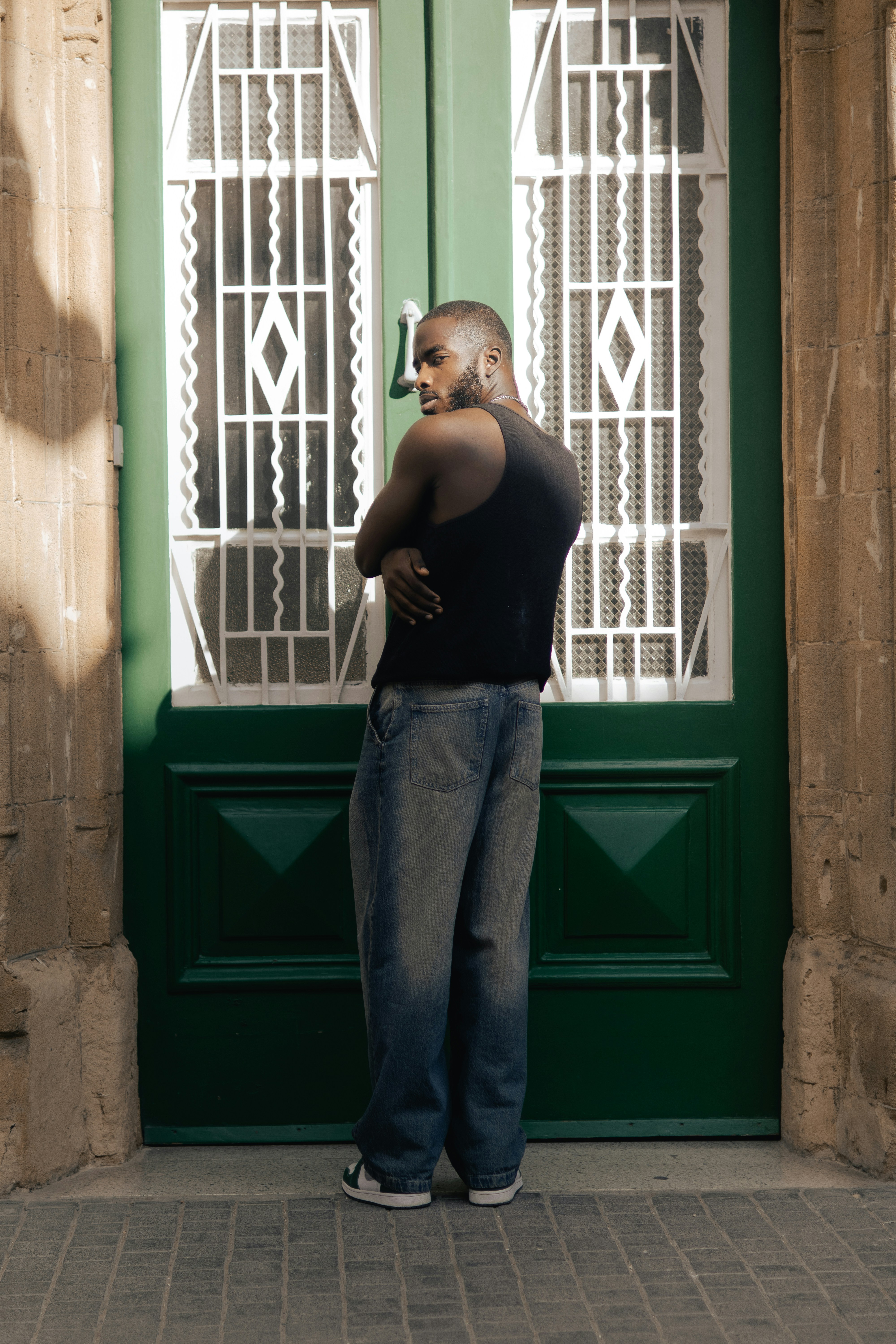 Man in tank top and jeans standing by green doors.