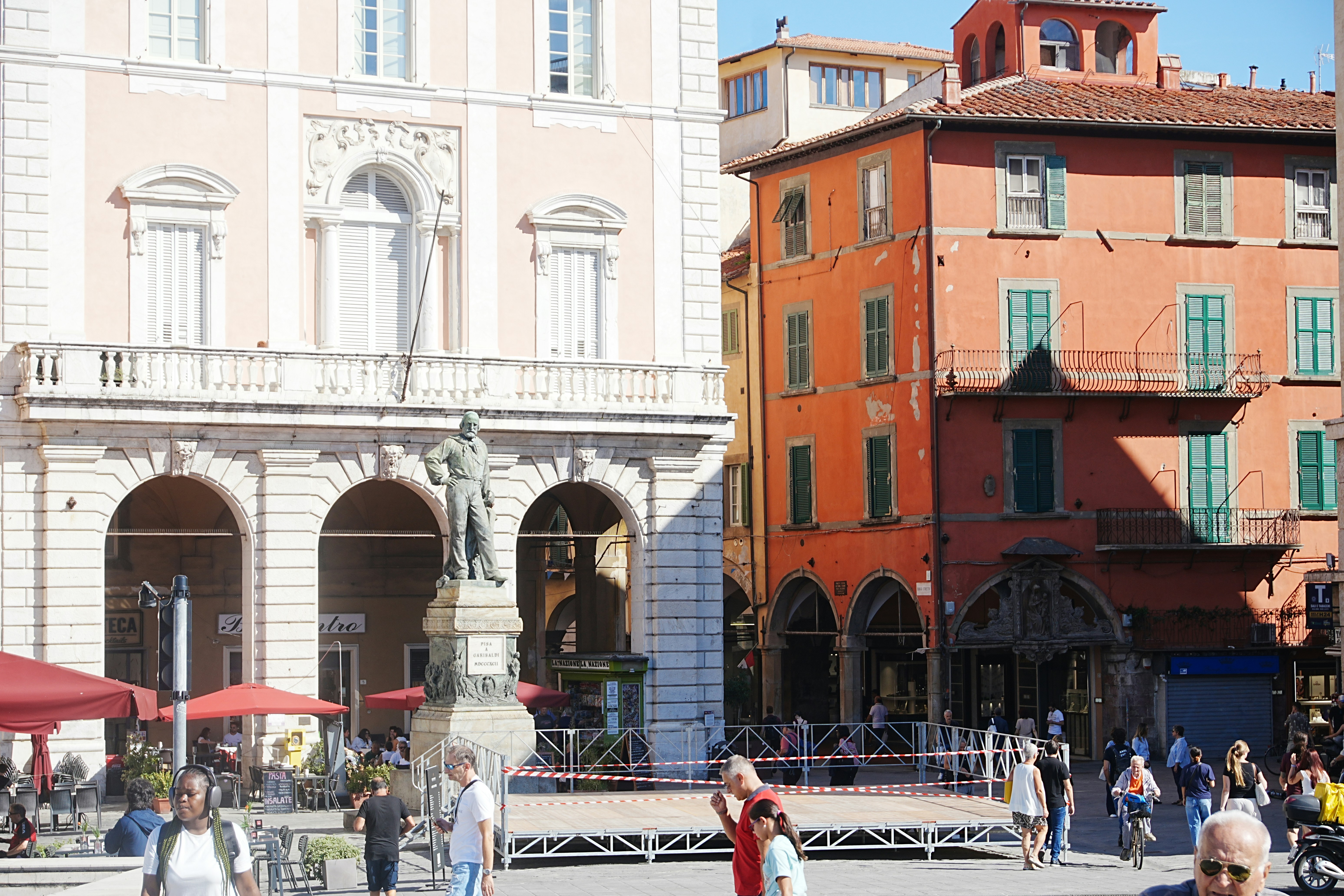 A lively square featuring a prominent statue and colorful buildings, bustling with people enjoying the atmosphere.