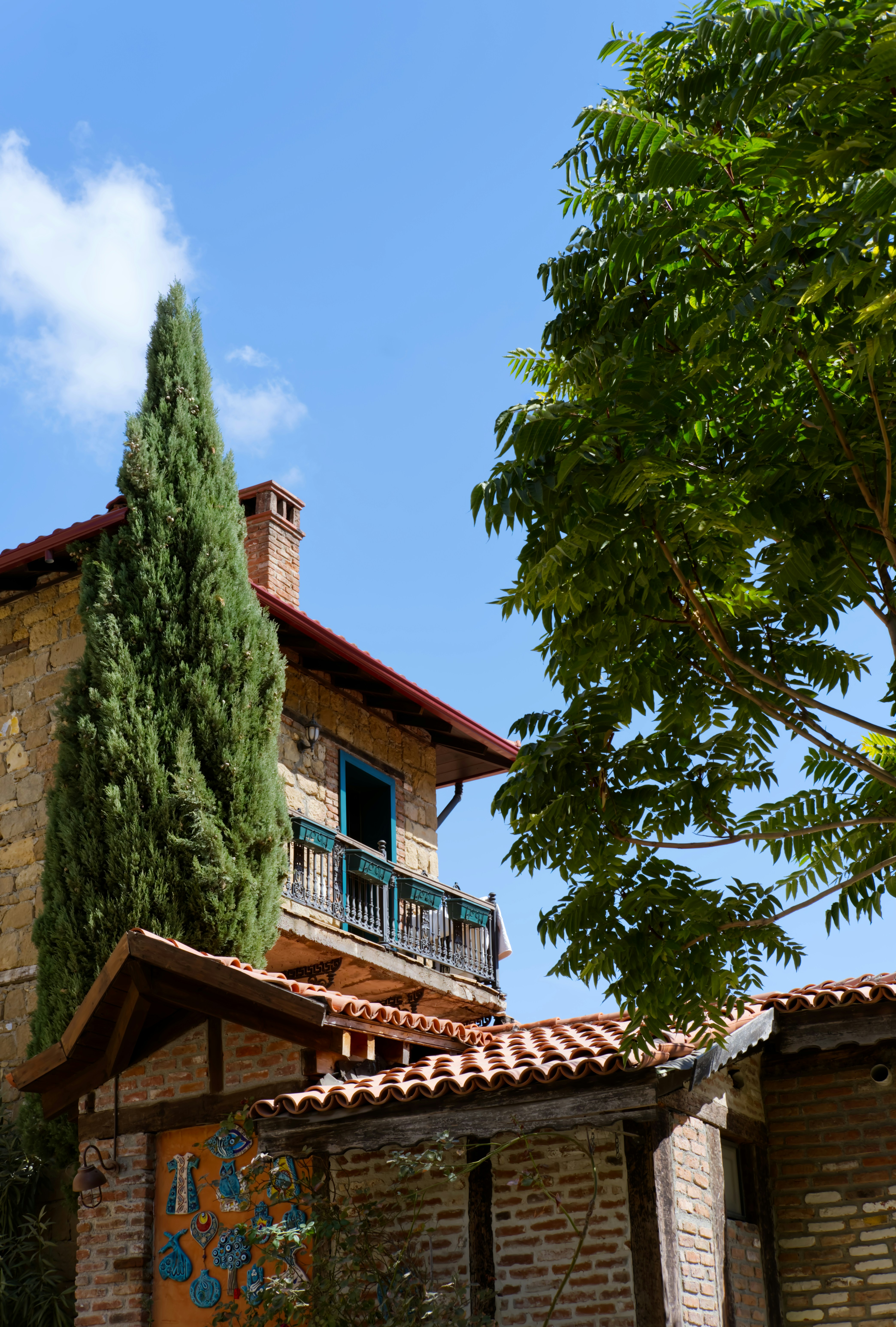 A picturesque stone house adorned with vibrant tiles and surrounded by lush greenery under a clear blue sky.