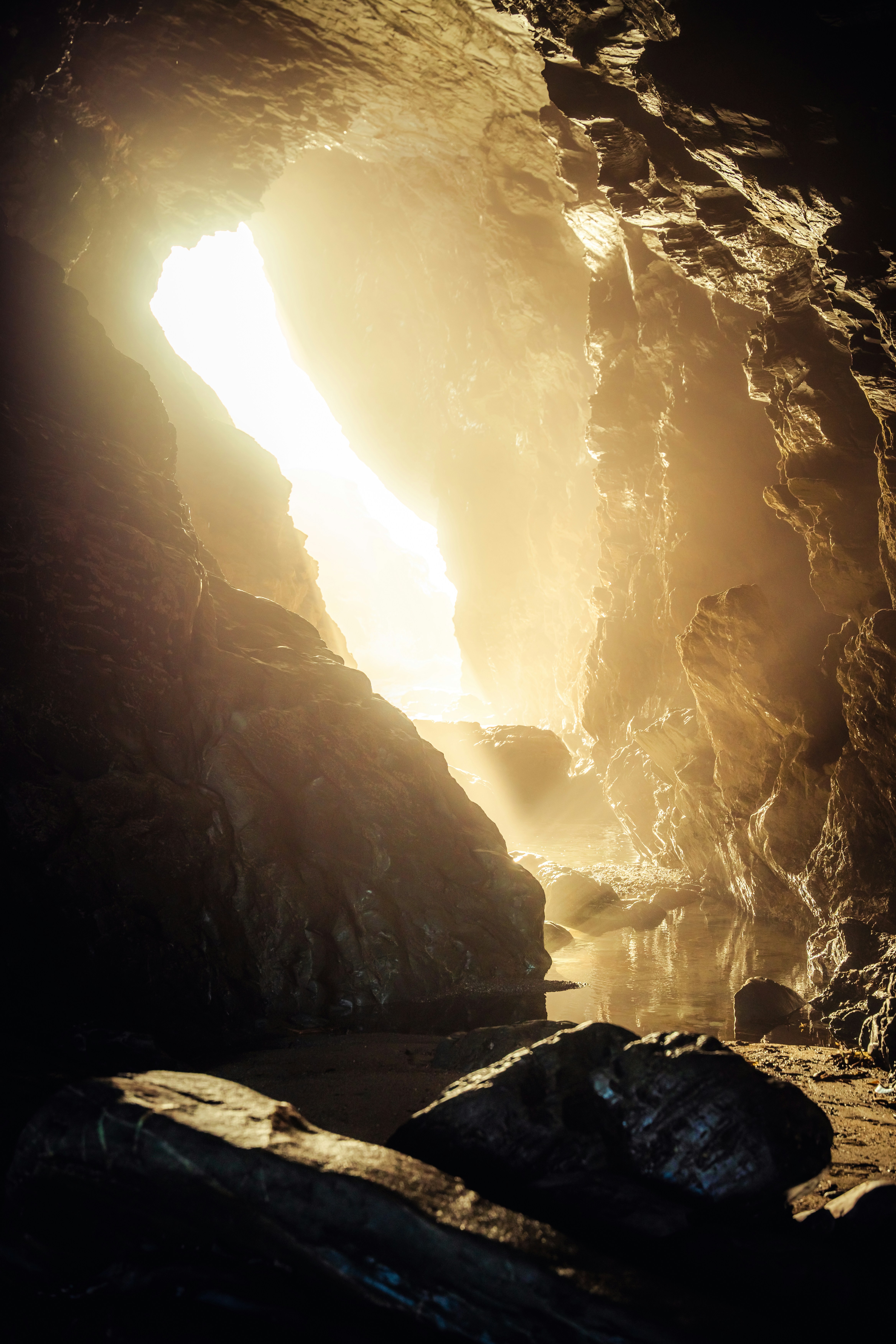 Sunlight streams into a dark, rocky cave entrance.
