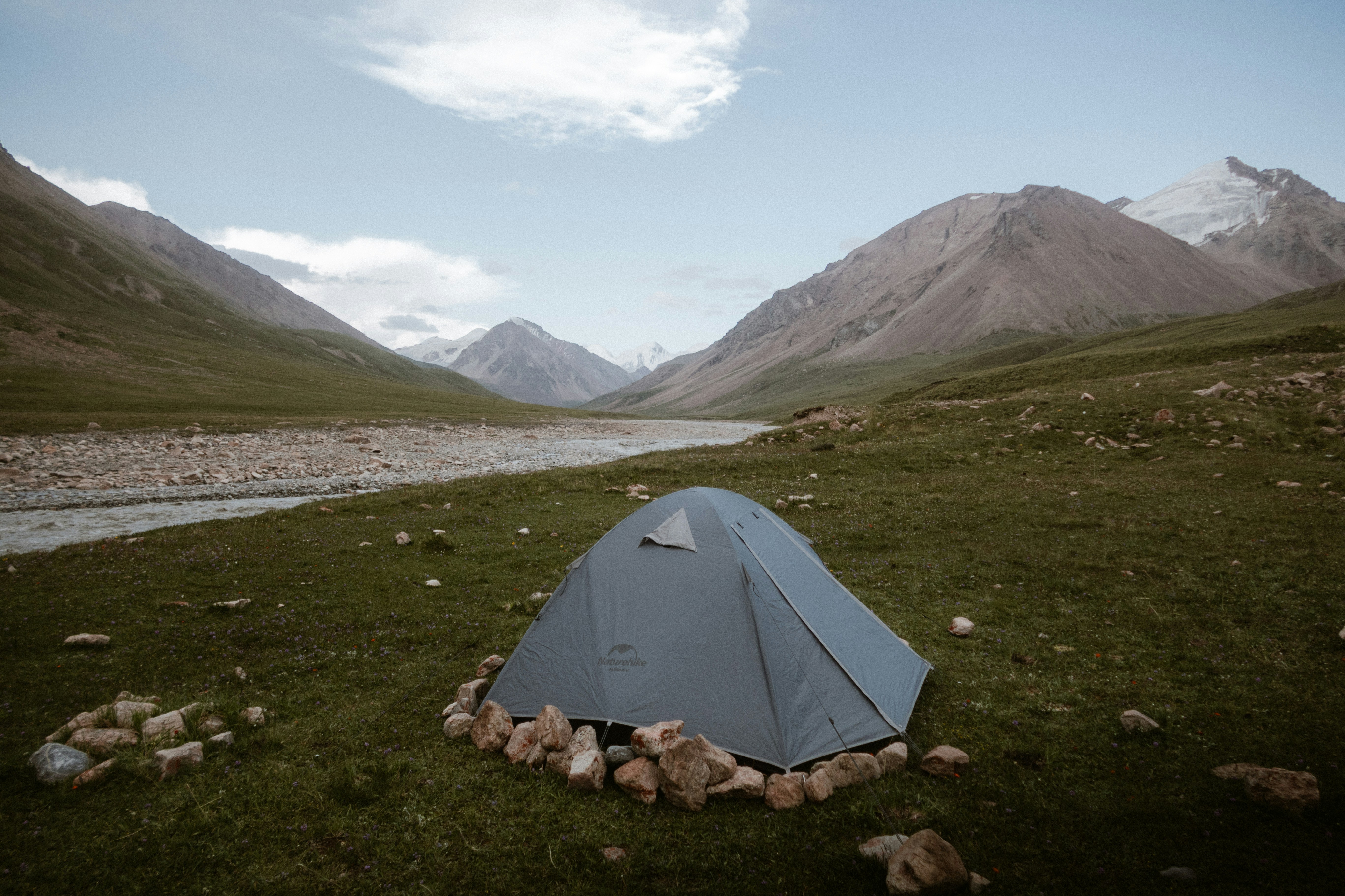 Tent set up in a grassy mountain valley with river.