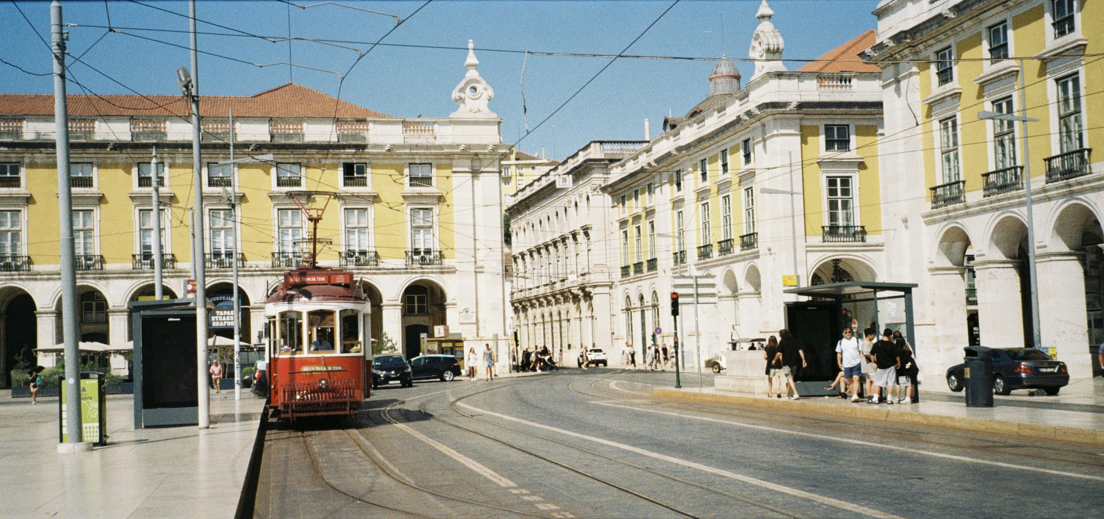 lisbon tram on main square captured on film | A red tram travels down a street in lisbon.