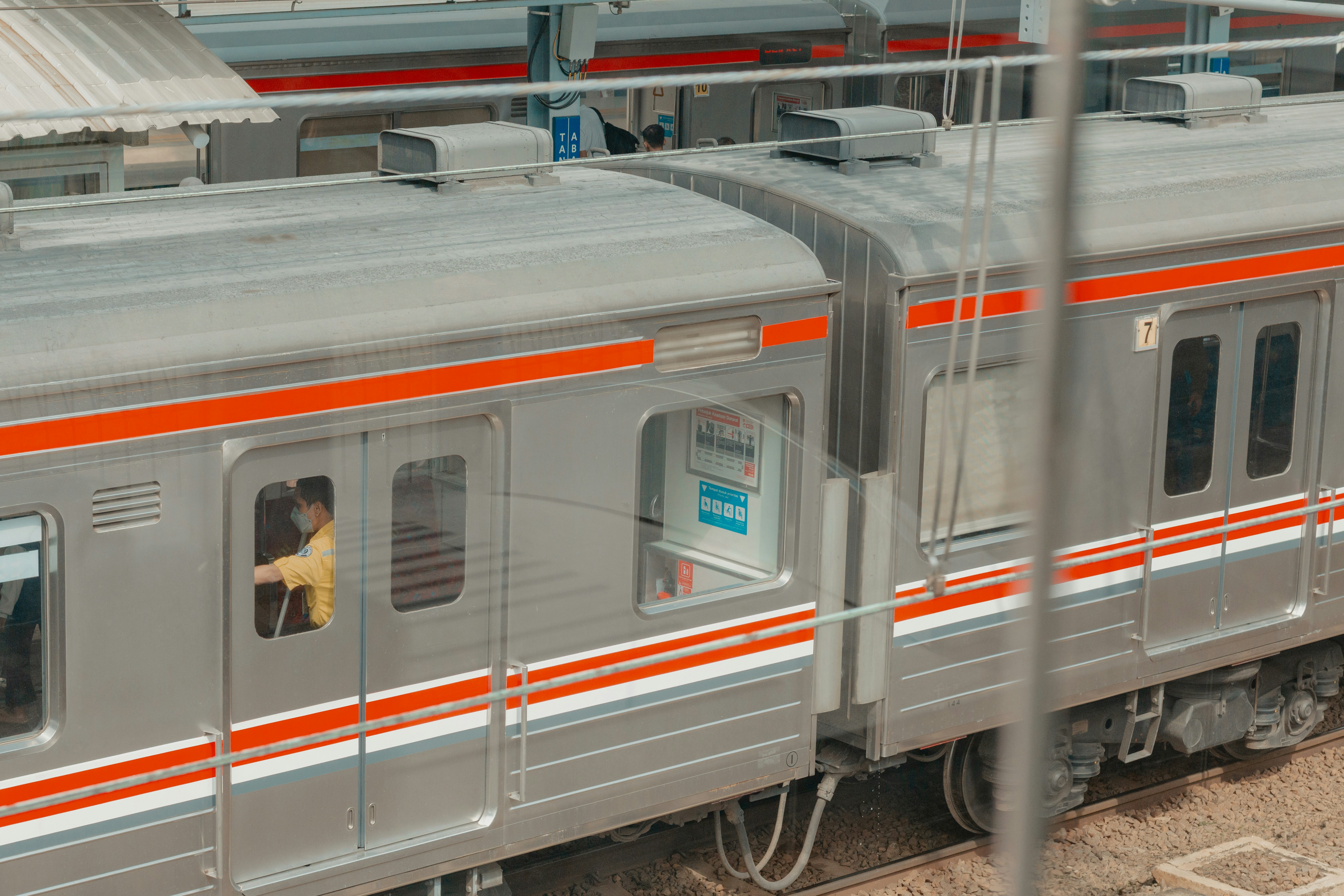 A close-up view of a train car at a station, featuring a passenger in a yellow shirt. The train's sleek design and vibrant stripes emphasize modern urban transit.