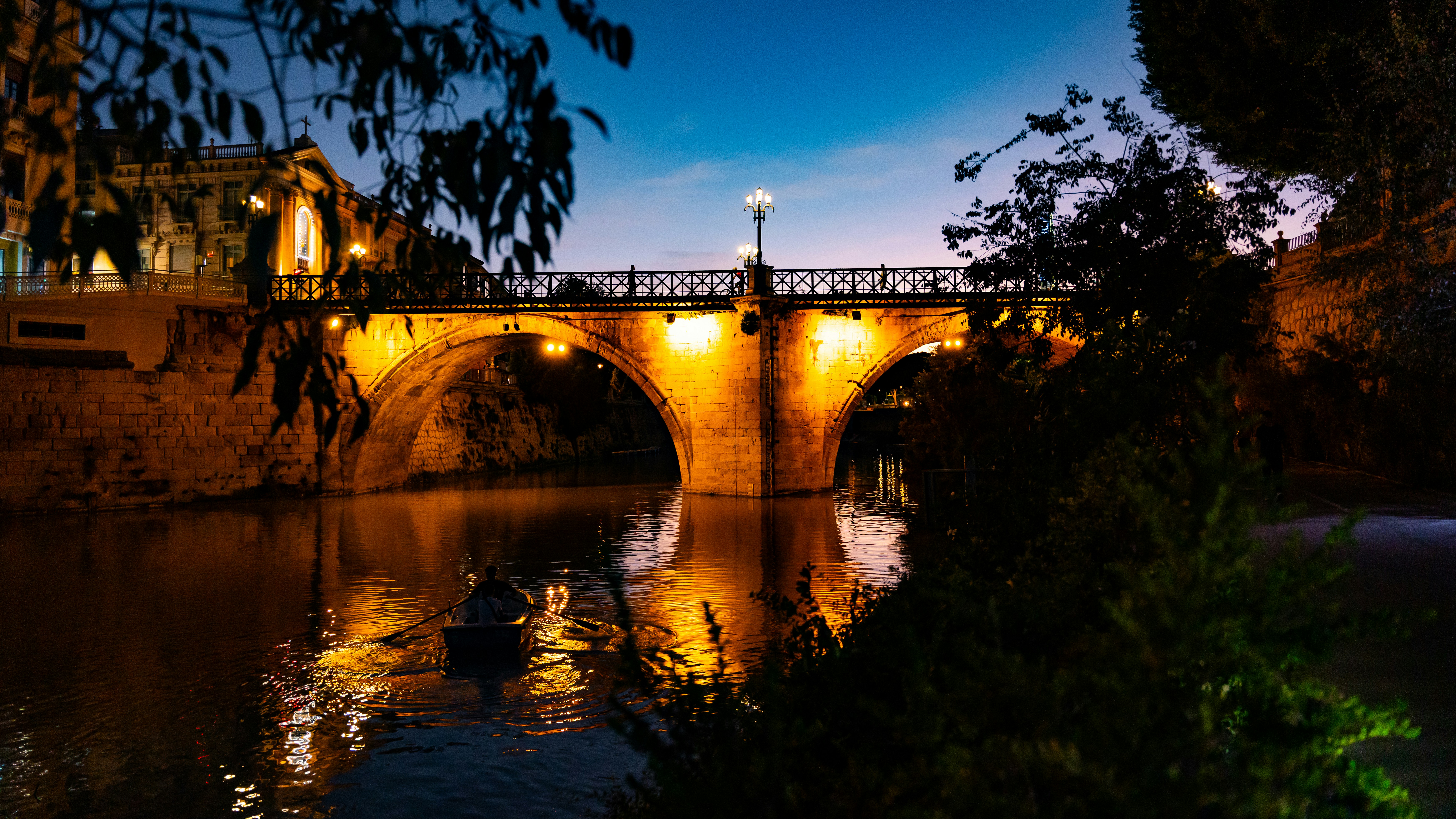 Shot of a traditional bridge near a park at sunset with orange lights in Murcia, Spain.