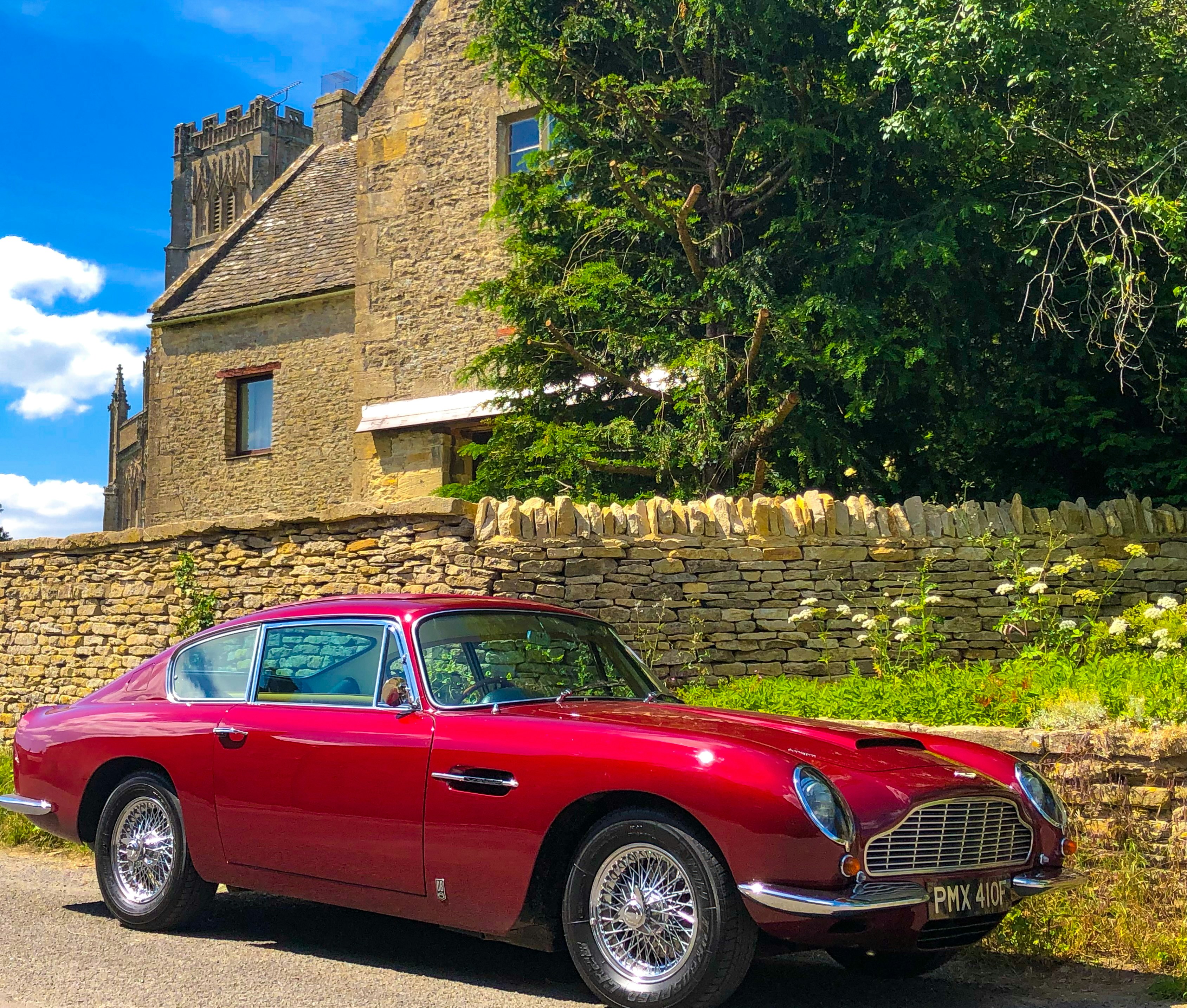 Vintage red sports car parked by stone building.