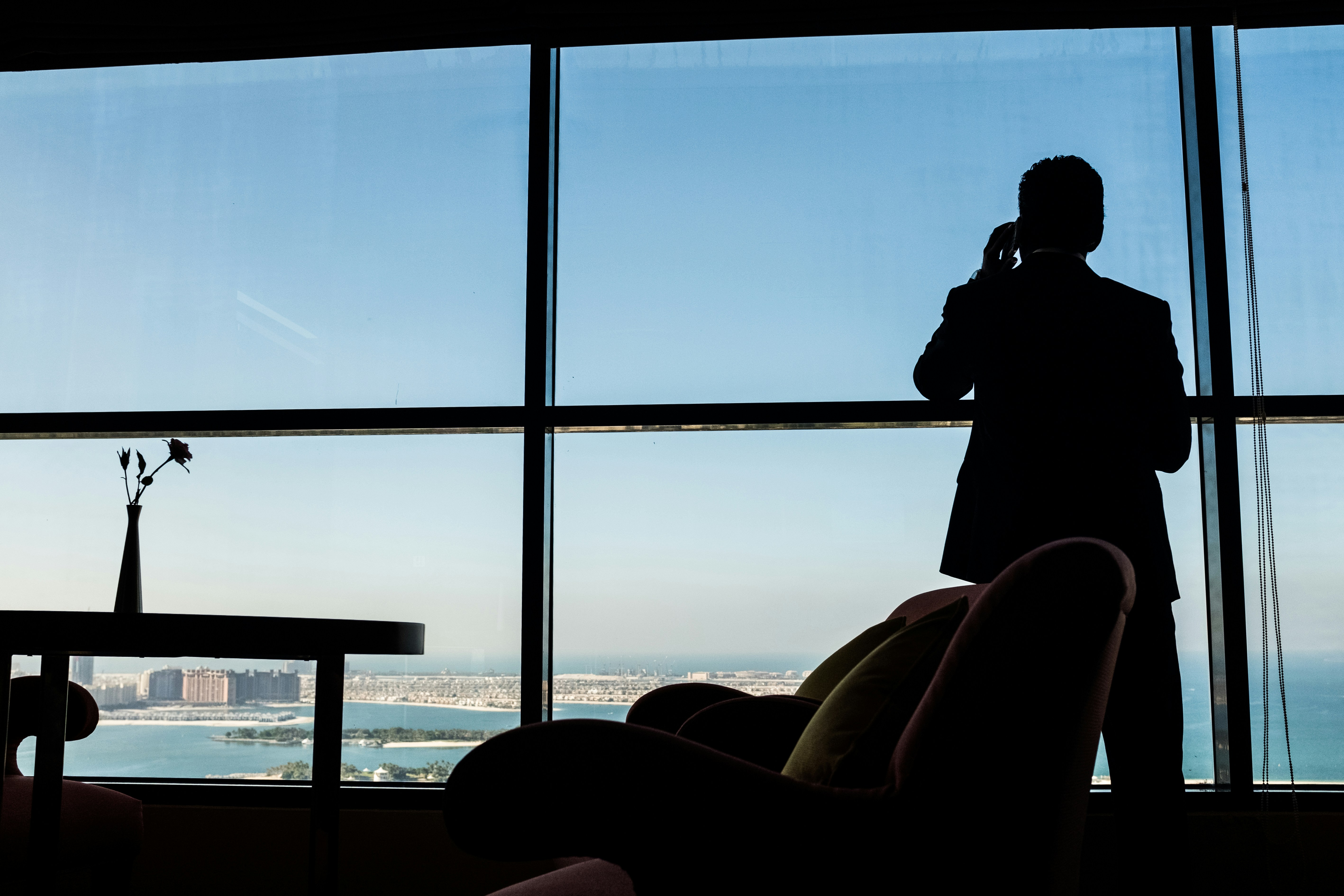 Man in suit talking on phone by large window.