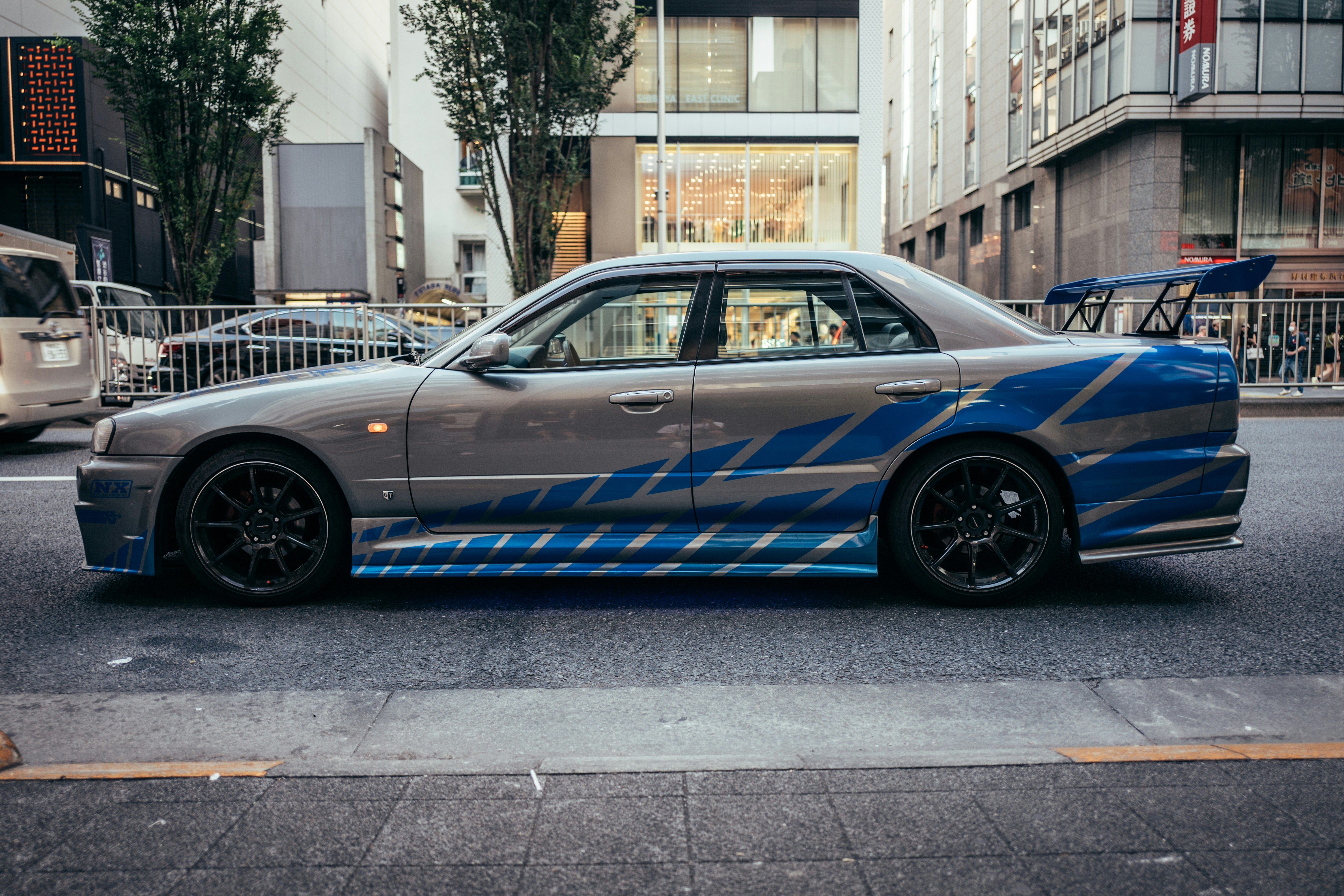 Tuned gray sedan with blue racing stripes on street.