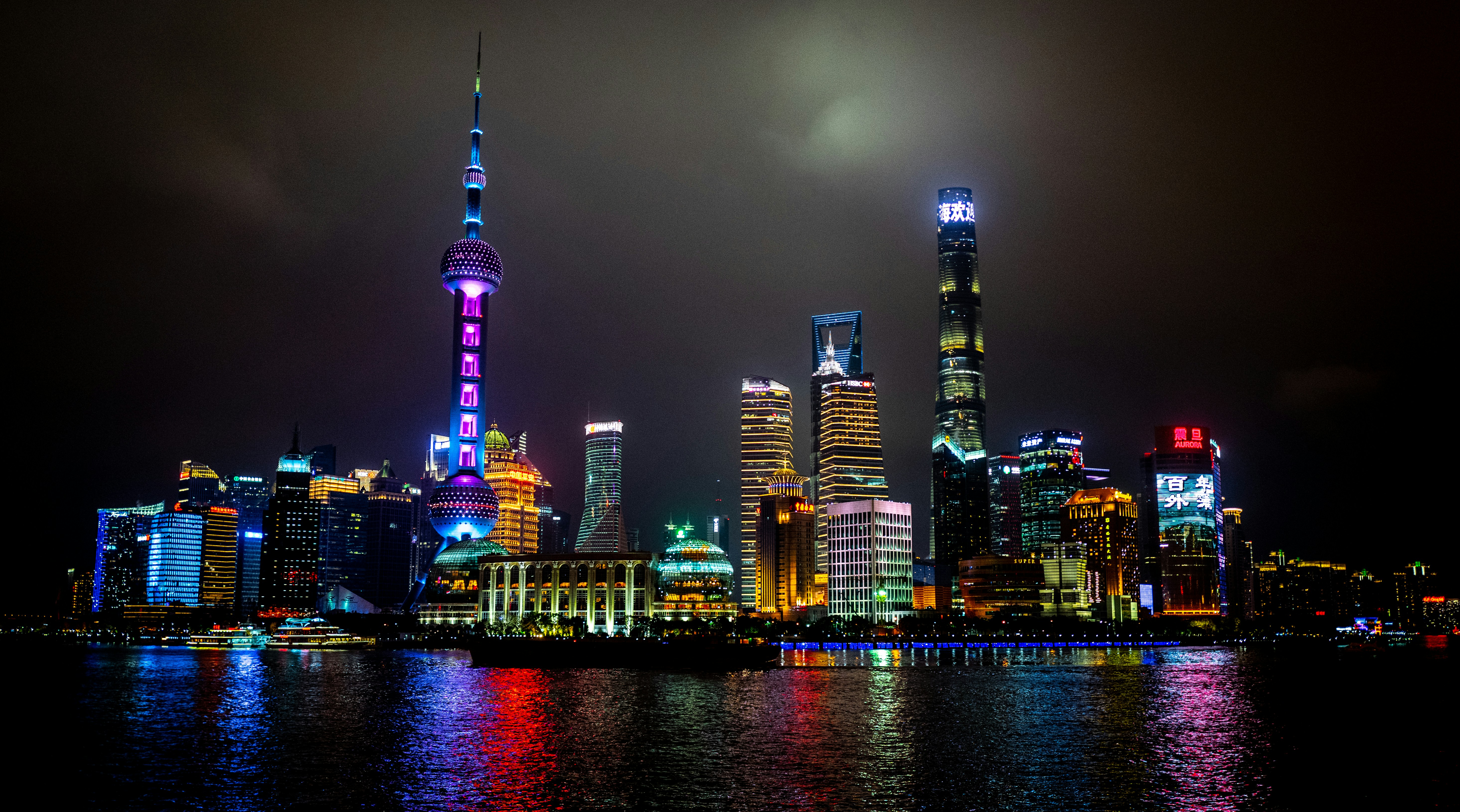 Vibrant skyline of Shanghai illuminated at night, showcasing iconic skyscrapers and their reflections on the water's surface.