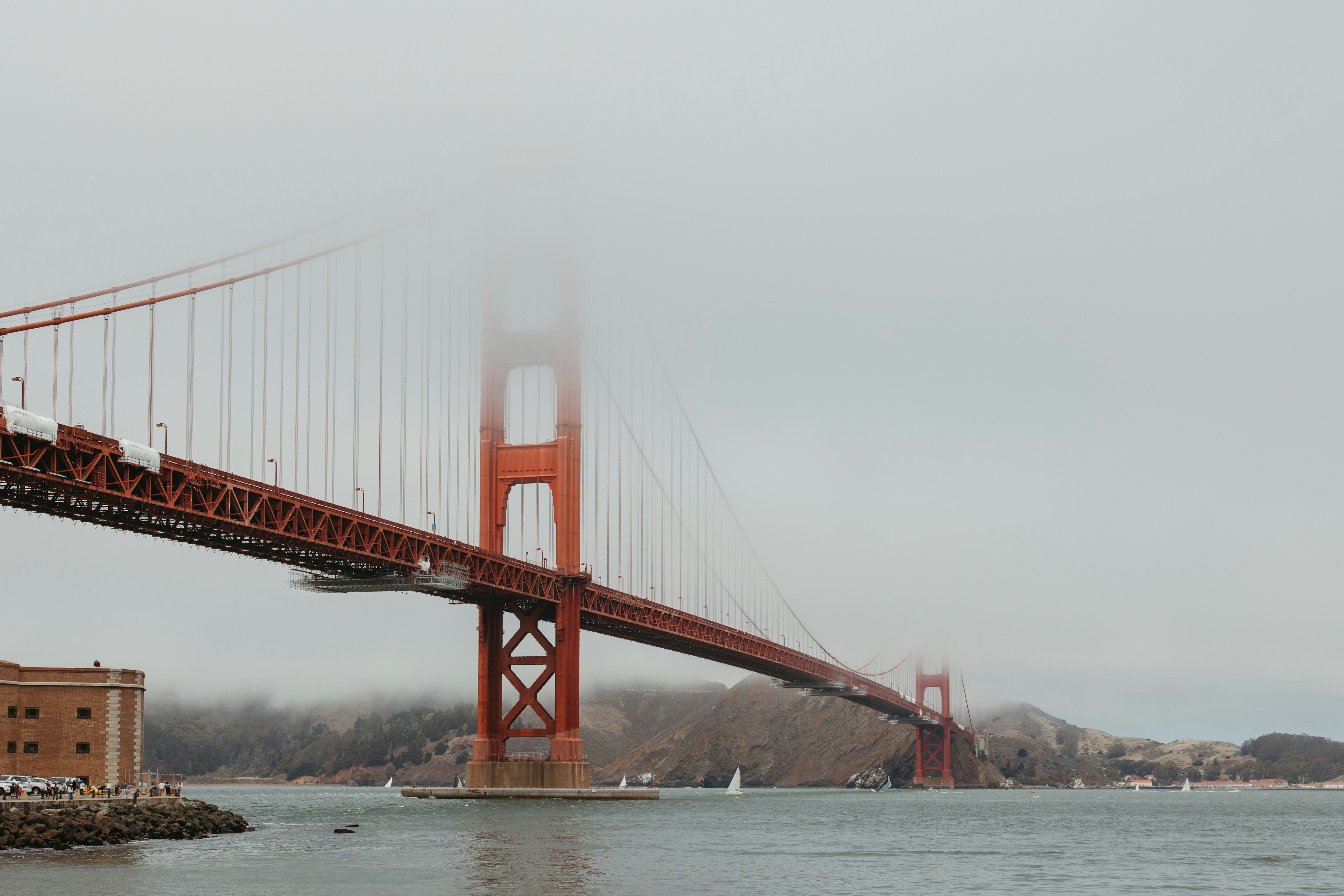 Golden gate bridge shrouded in fog over water.