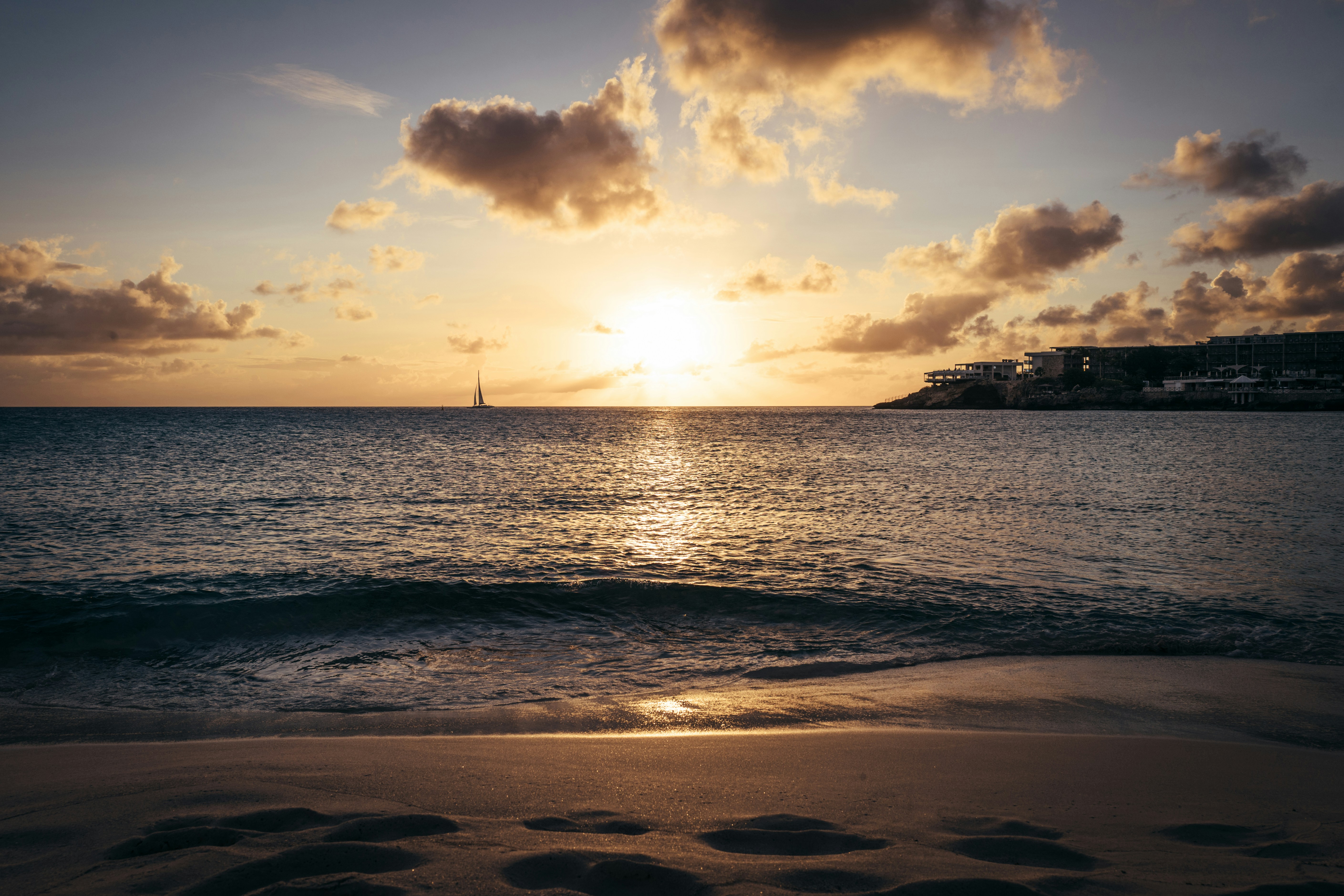 Sunset over a calm ocean with distant buildings.