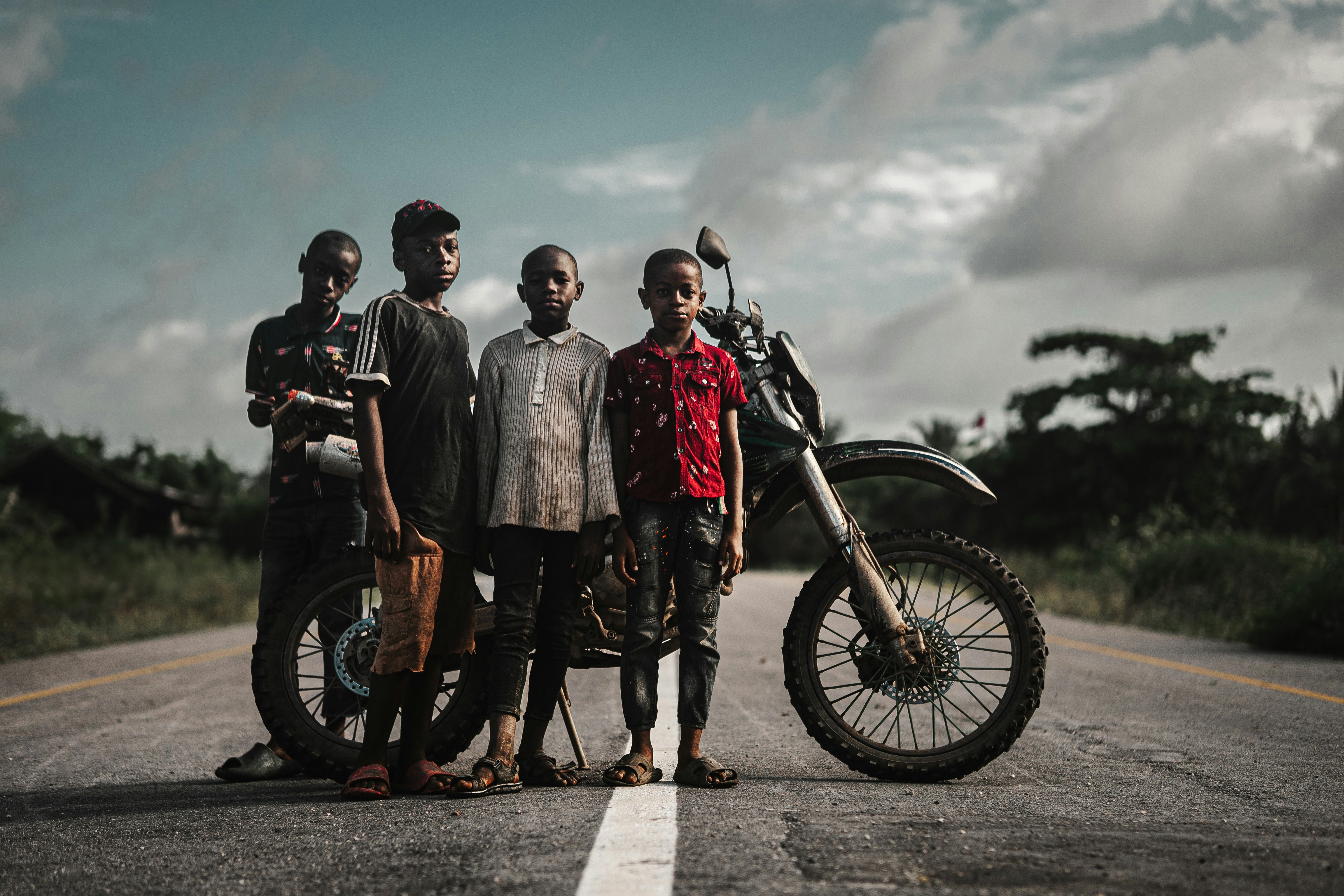 Four African boys with an off-road motorcycle | Four boys stand with a dirt bike on a road.