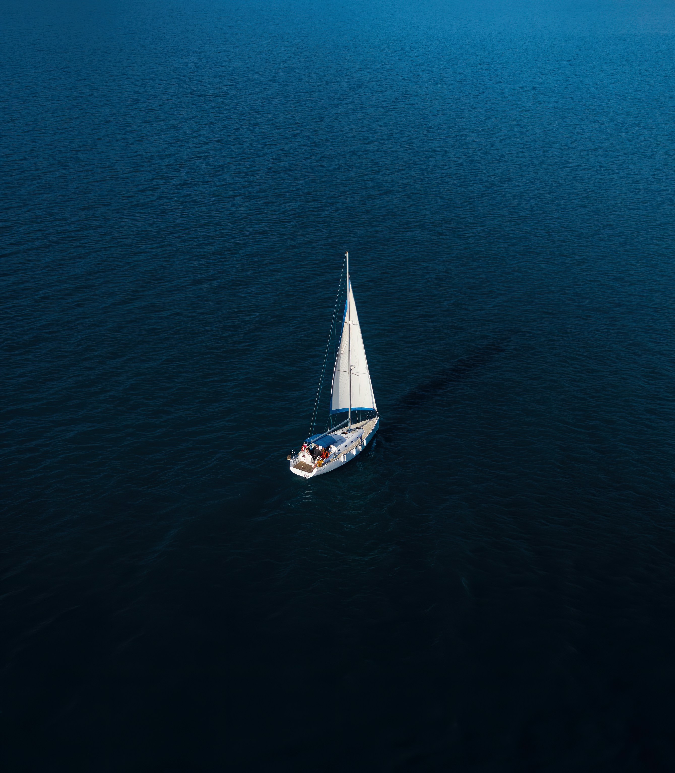 A lone sailboat glides across a deep blue ocean.
