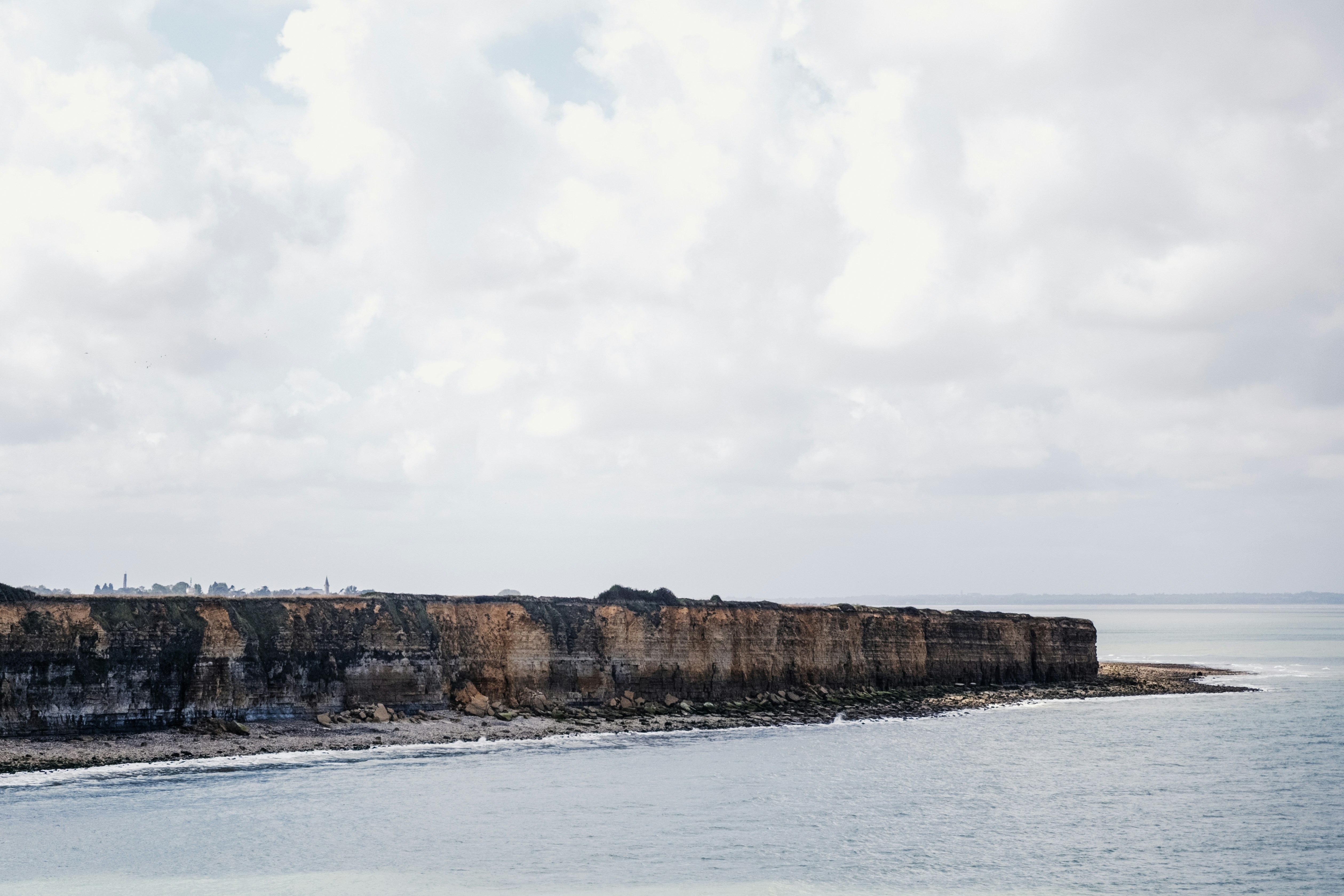 Rocky cliff face meets the calm ocean under cloudy sky