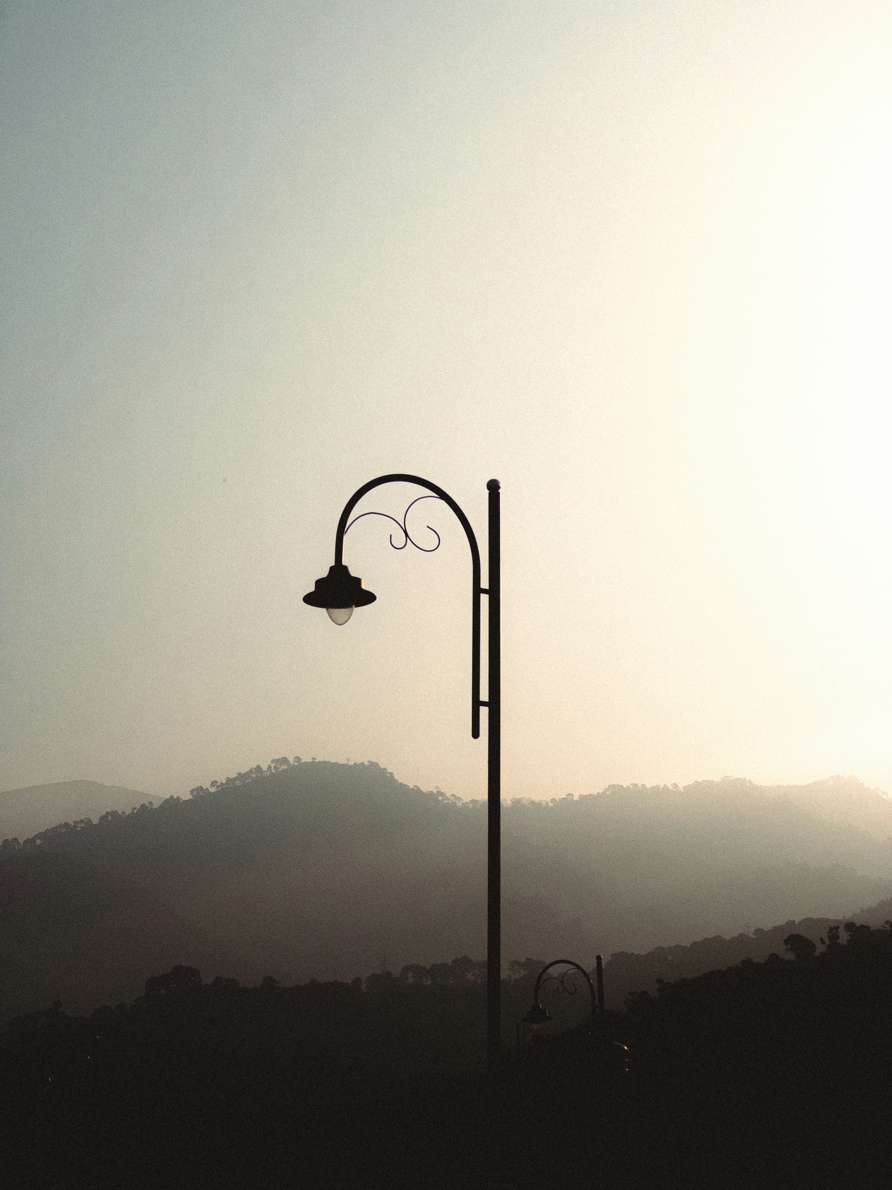 Street lamp silhouetted against a hazy mountain landscape.