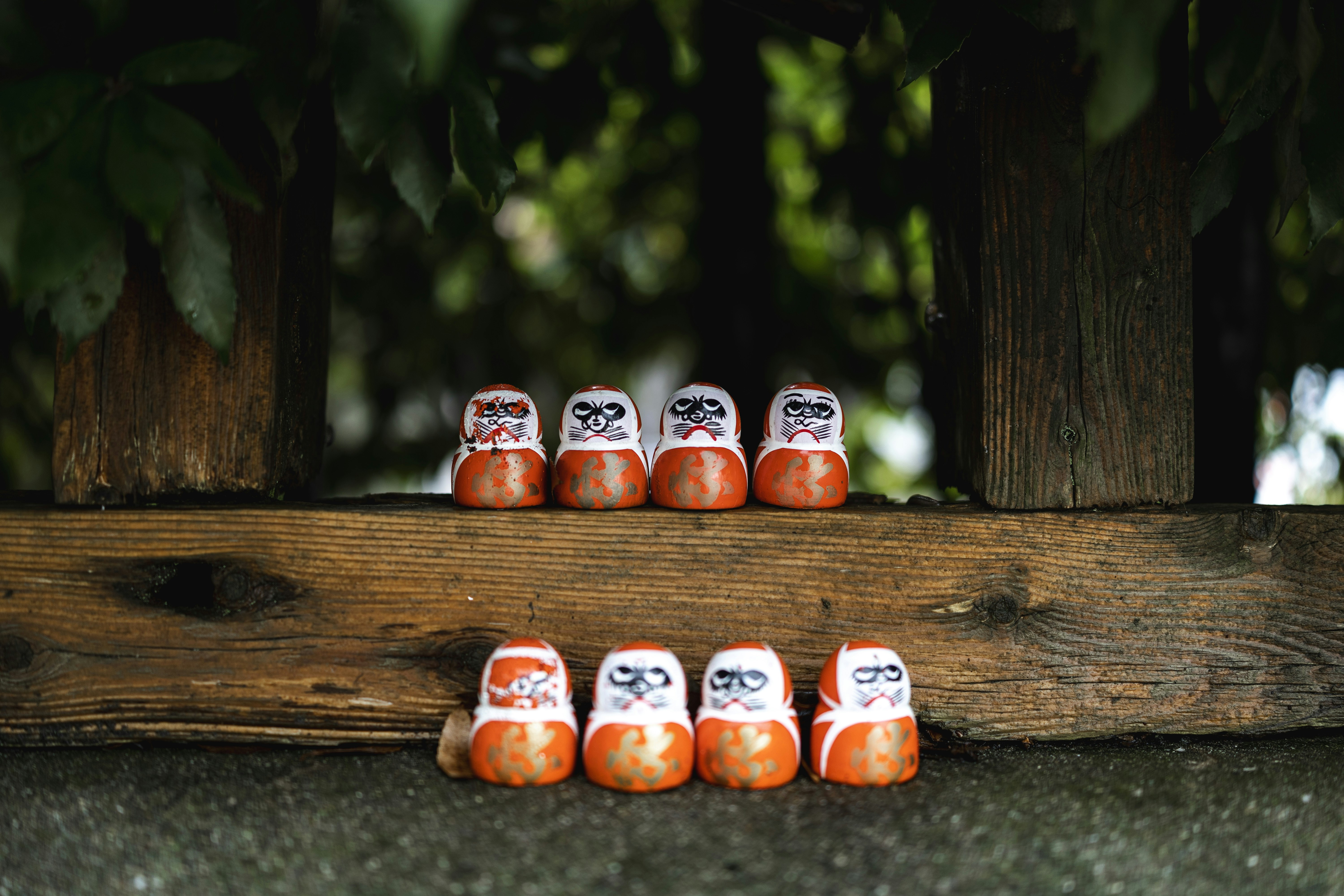 Row of Matryoshka-style Daruma dolls peeking from under a wooden railing