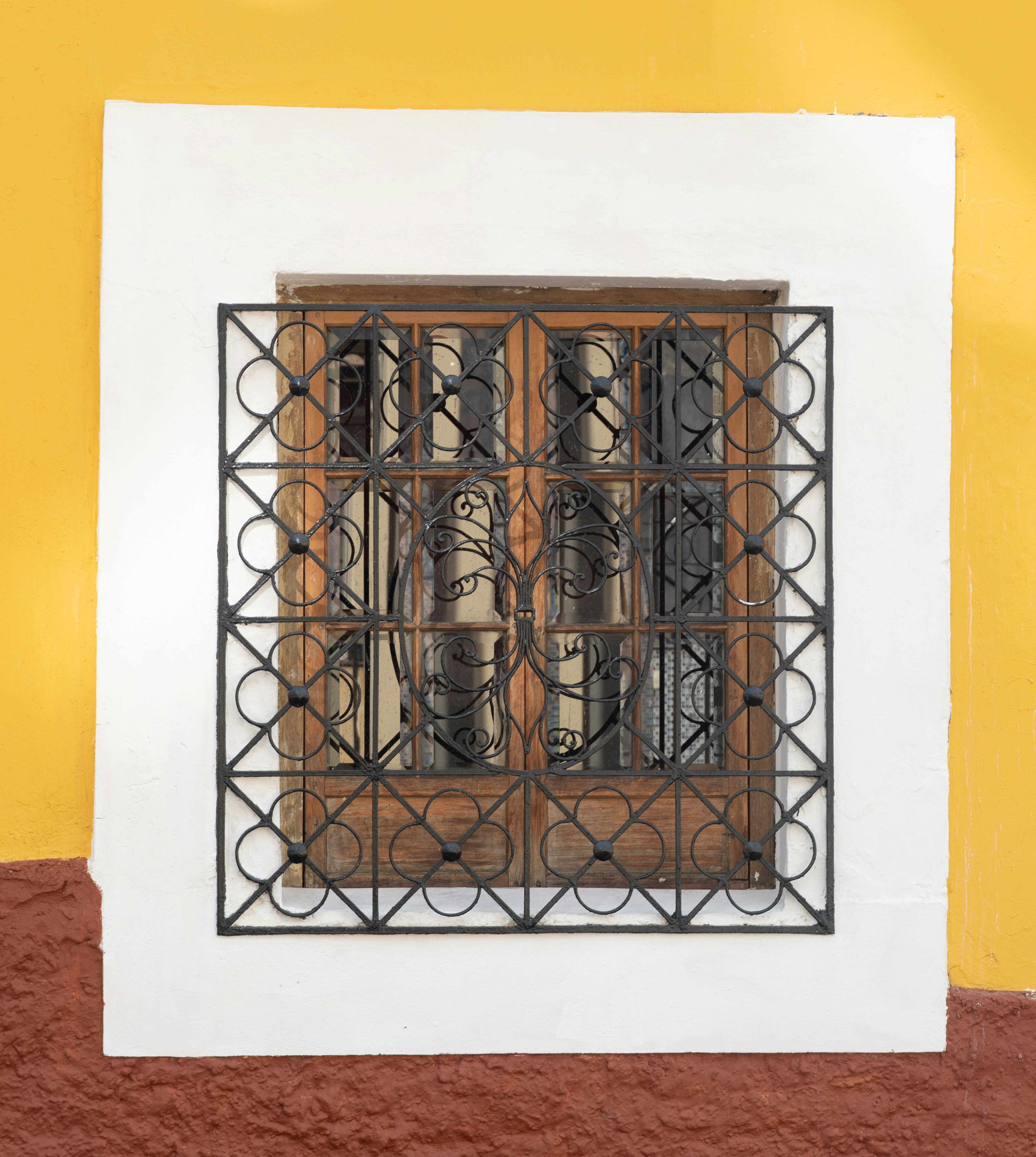 Ornate Iron Grille Framing a Window on a Sunlit Yellow Facade