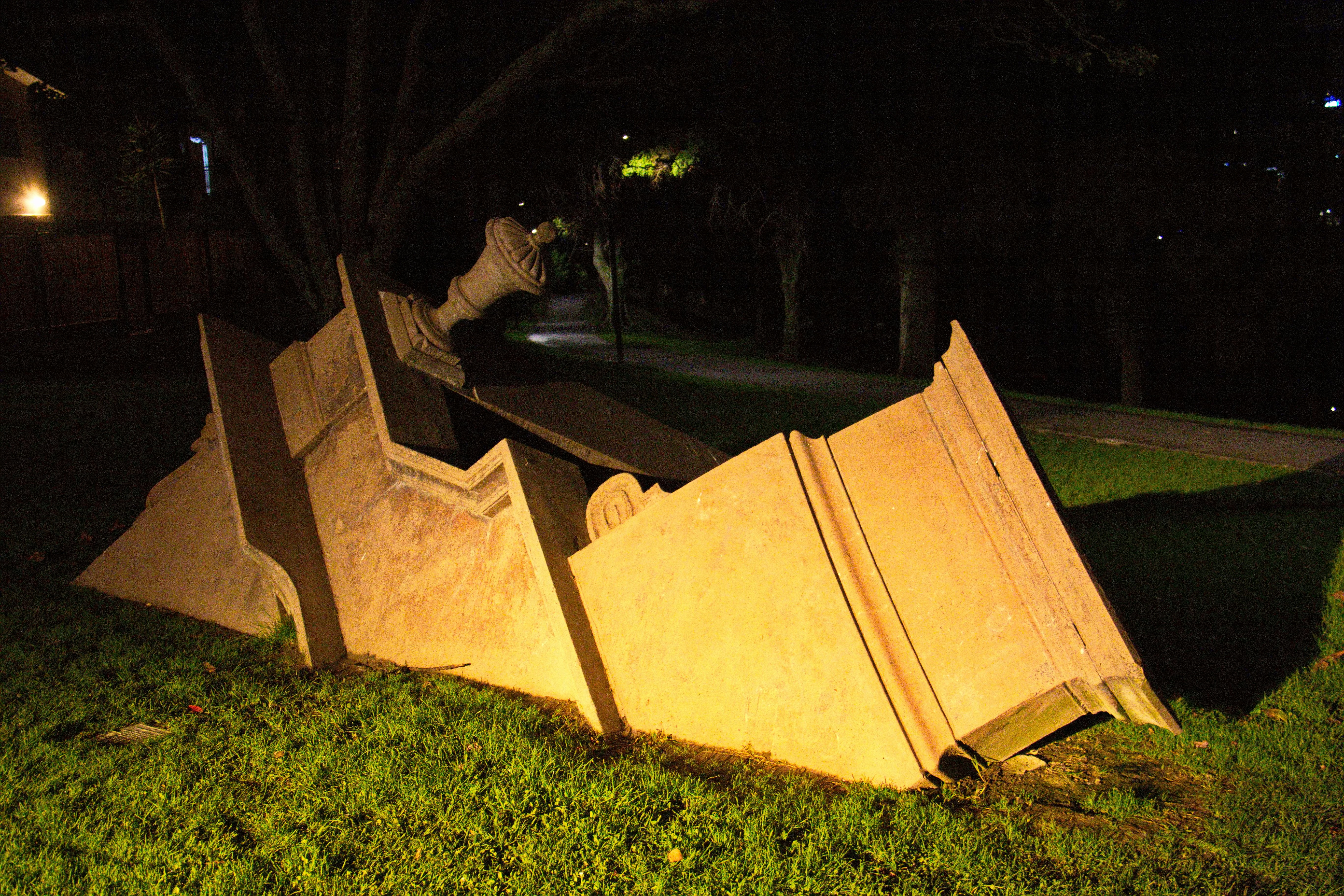 Broken concrete structure lying on grassy area at night.