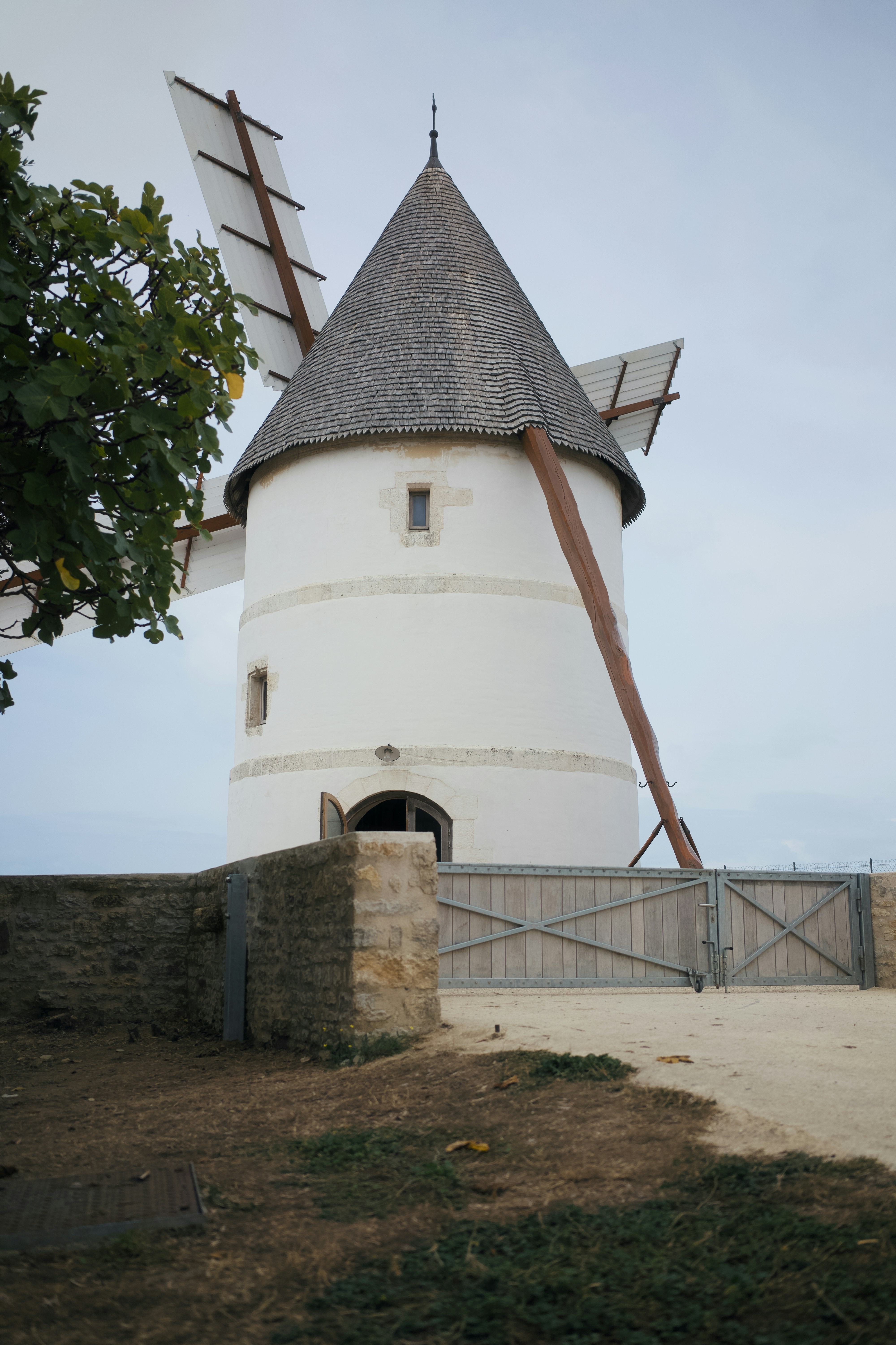 A white windmill with wooden sails and a conical roof.