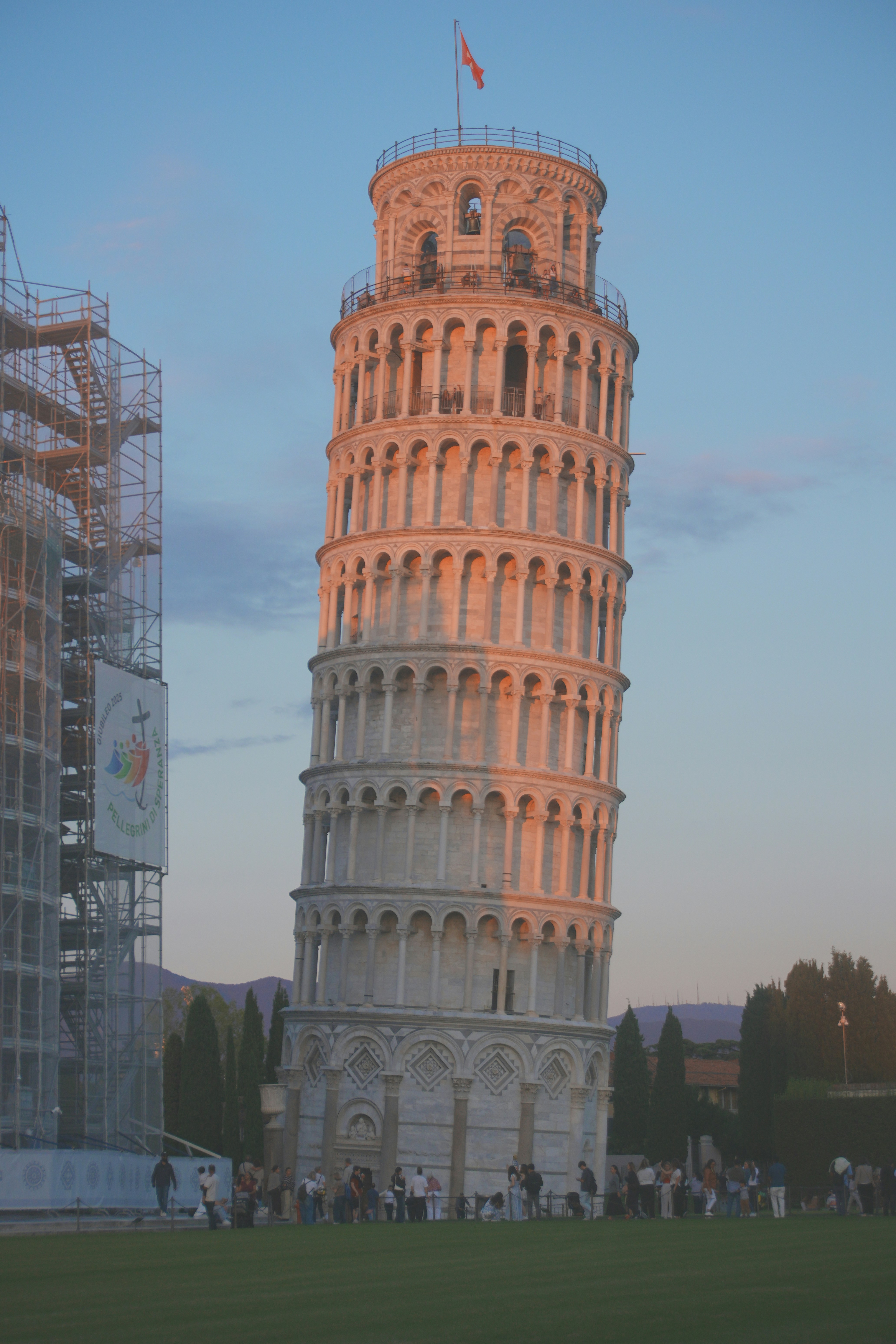 Leaning Tower of Pisa illuminated by the warm hues of sunset, surrounded by scaffolding and visitors admiring its unique architecture.