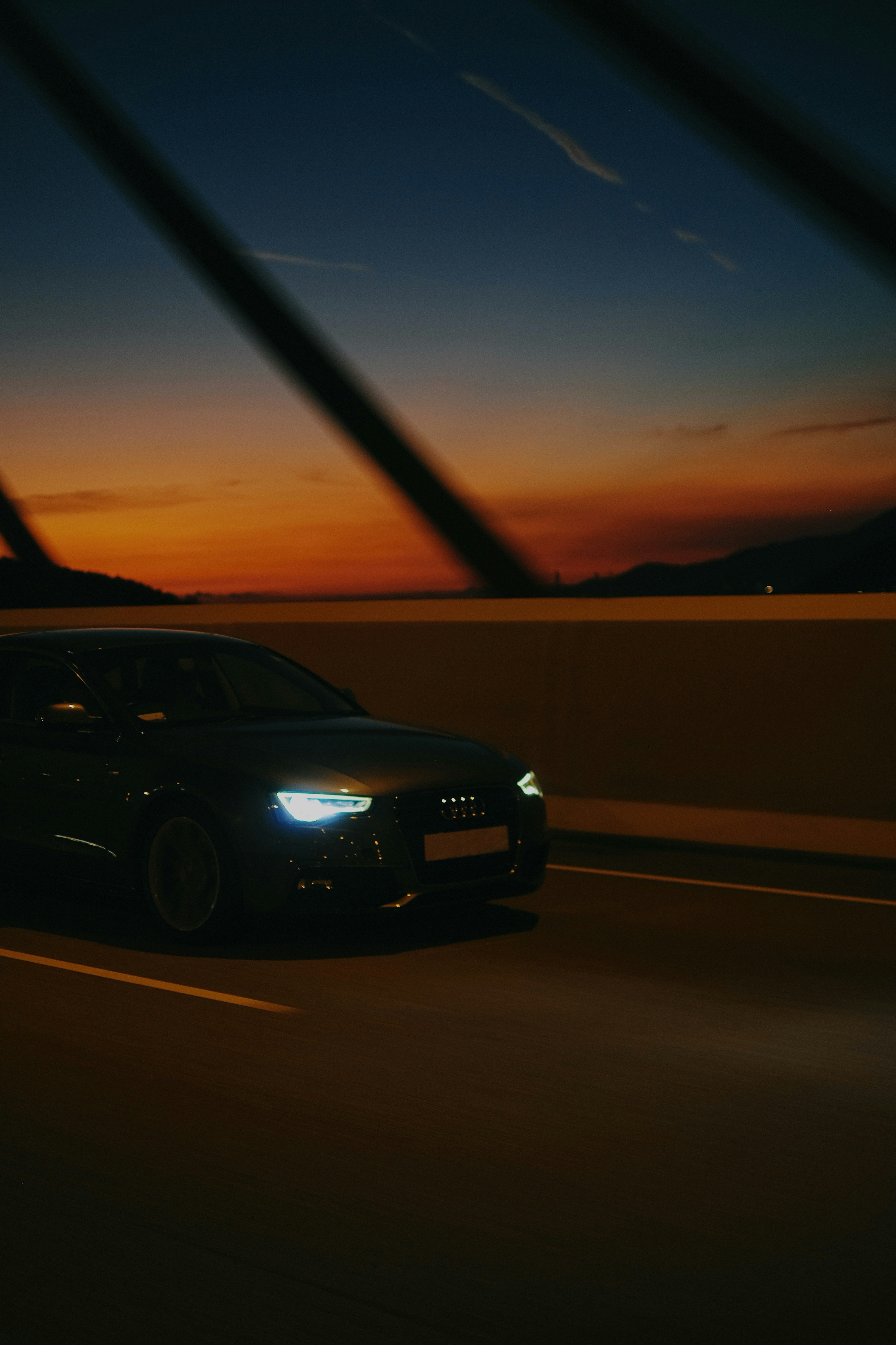 Black car driving on a bridge at sunset.